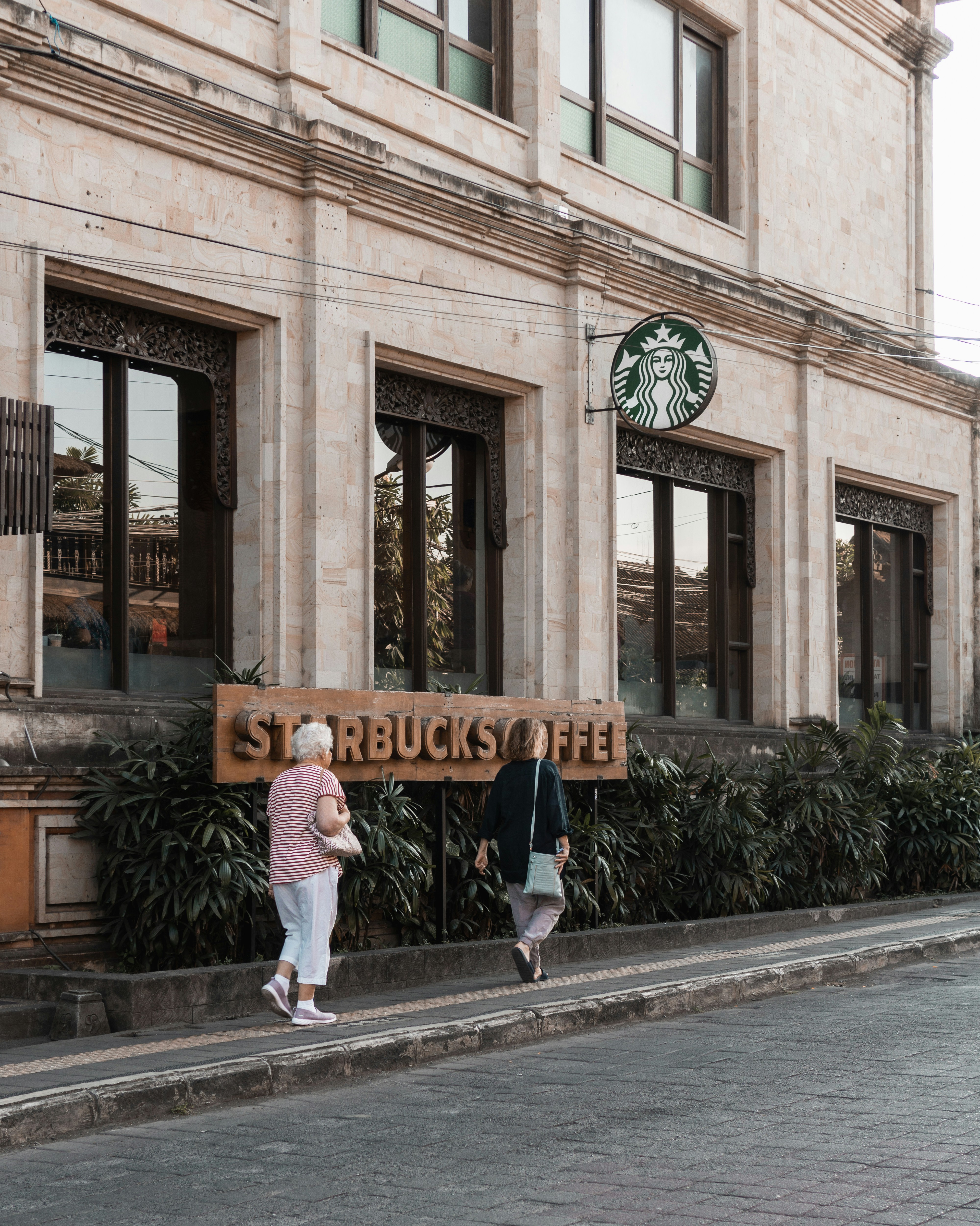 Stone Facade Rendezvous: Two Pedestrians Pass a Starbucks on a Quiet Street
