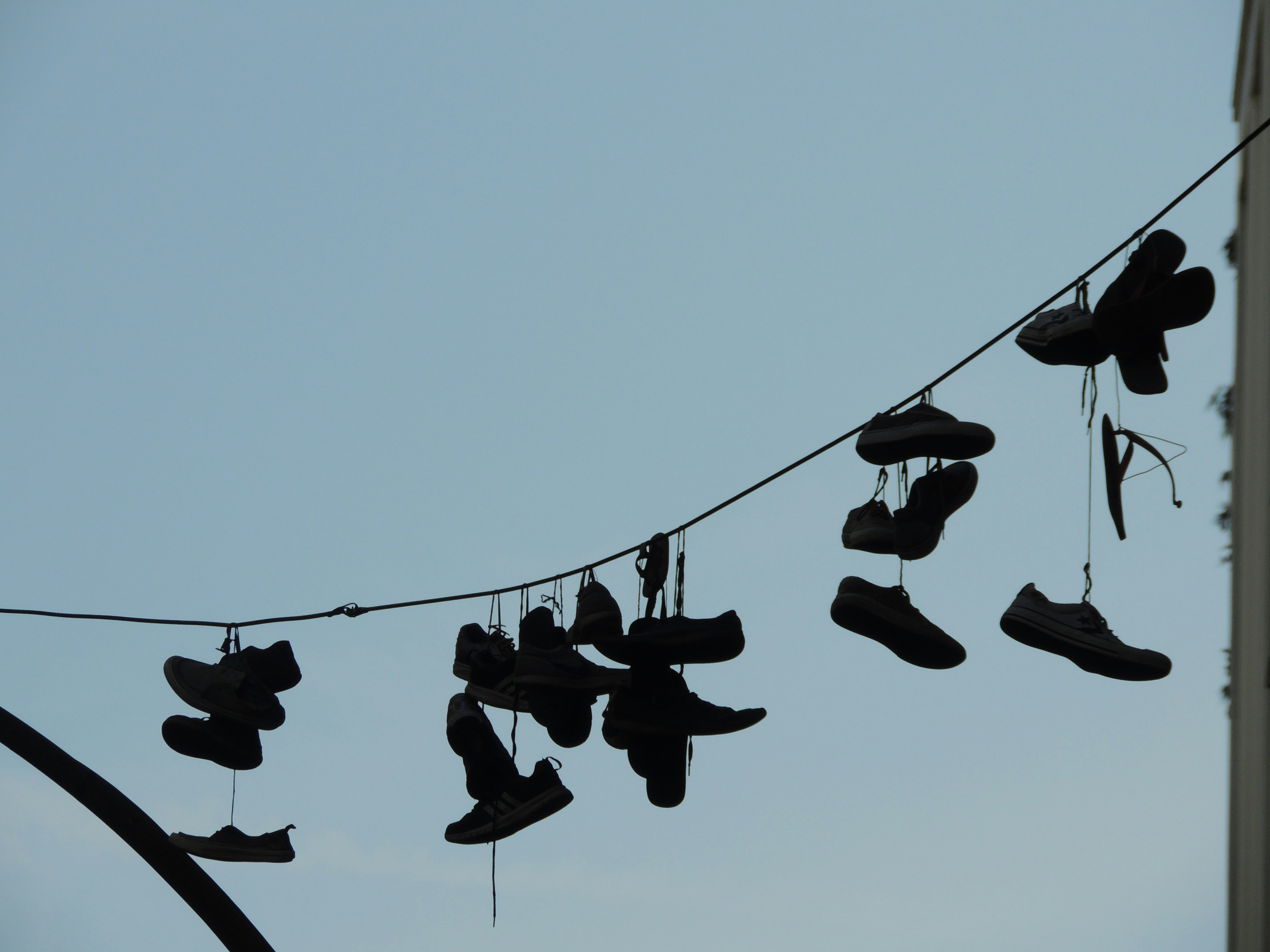 Silhouetted shoes hanging from a wire against a pale sky, symbolizing urban stories and forgotten journeys.