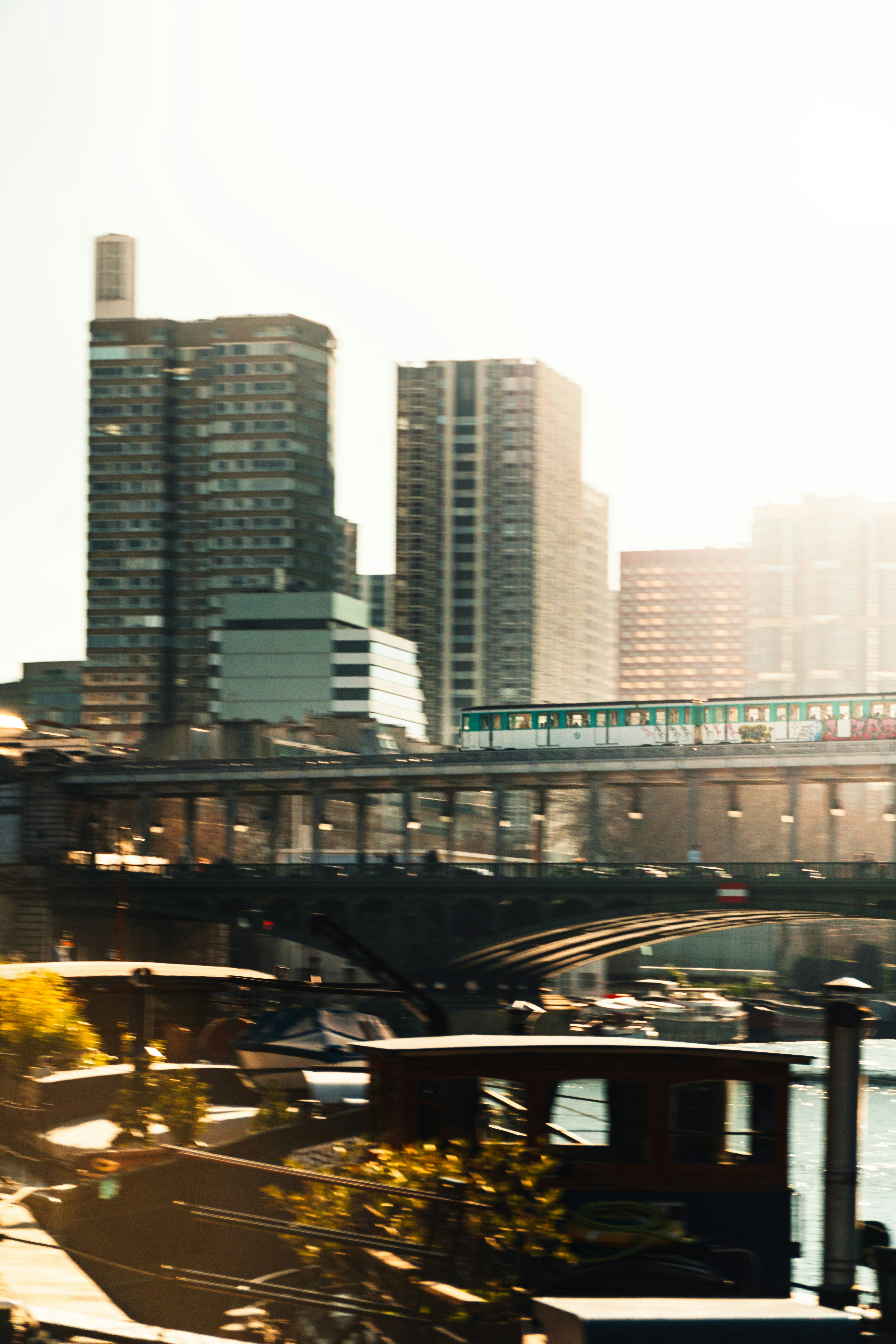 A vibrant city scene showcasing a train traversing a bridge amidst towering buildings, with a glimpse of waterfront life below.