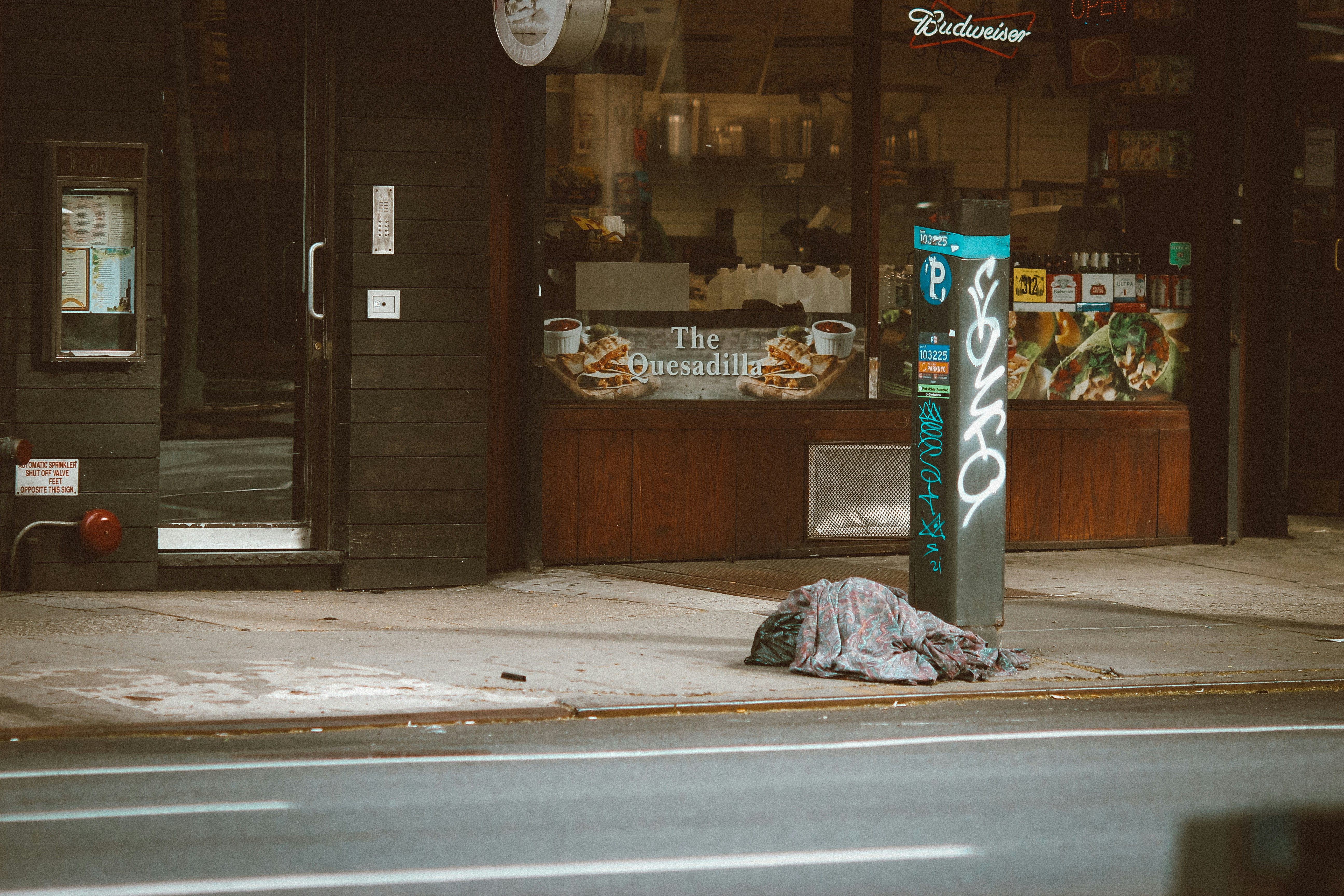 A tattered blanket lies abandoned on the sidewalk in front of a restaurant, hinting at the unseen stories of urban existence.