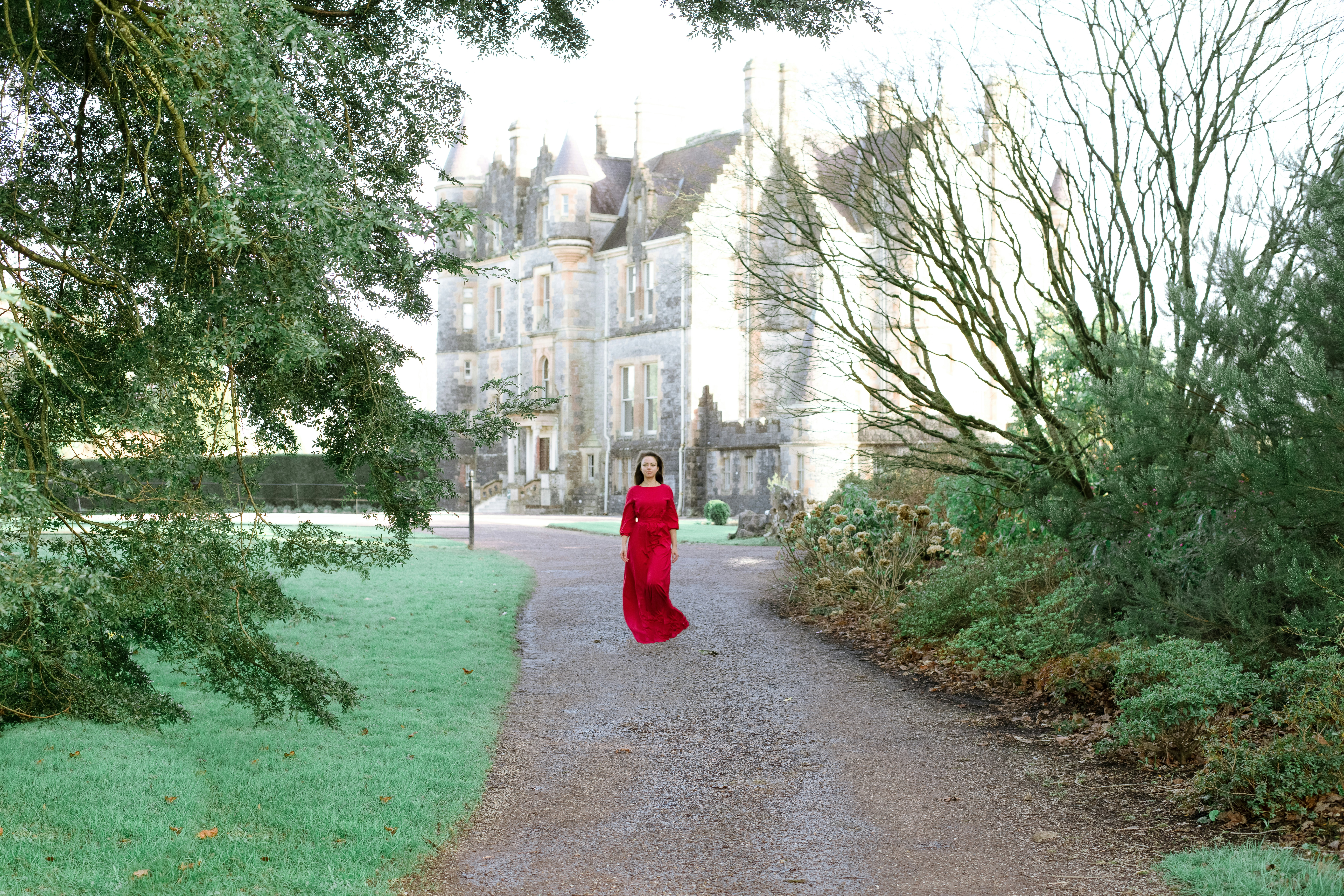 Crimson on Gravel: A Red-Dress Figure Traverses a Path to a Gothic Estate