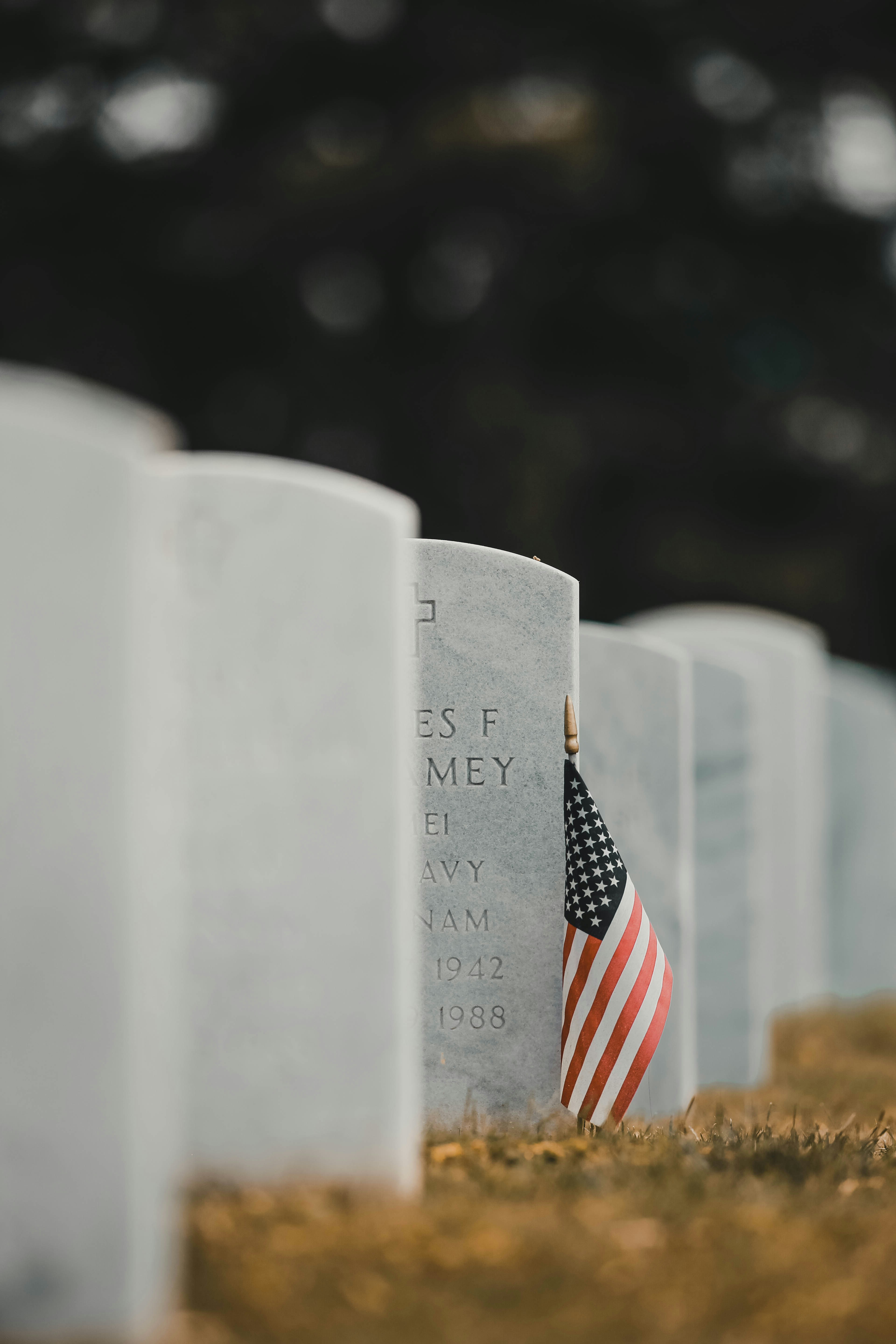 Marble gravestones lined in a cemetery, with an American flag placed at one grave, symbolizing remembrance and honor.