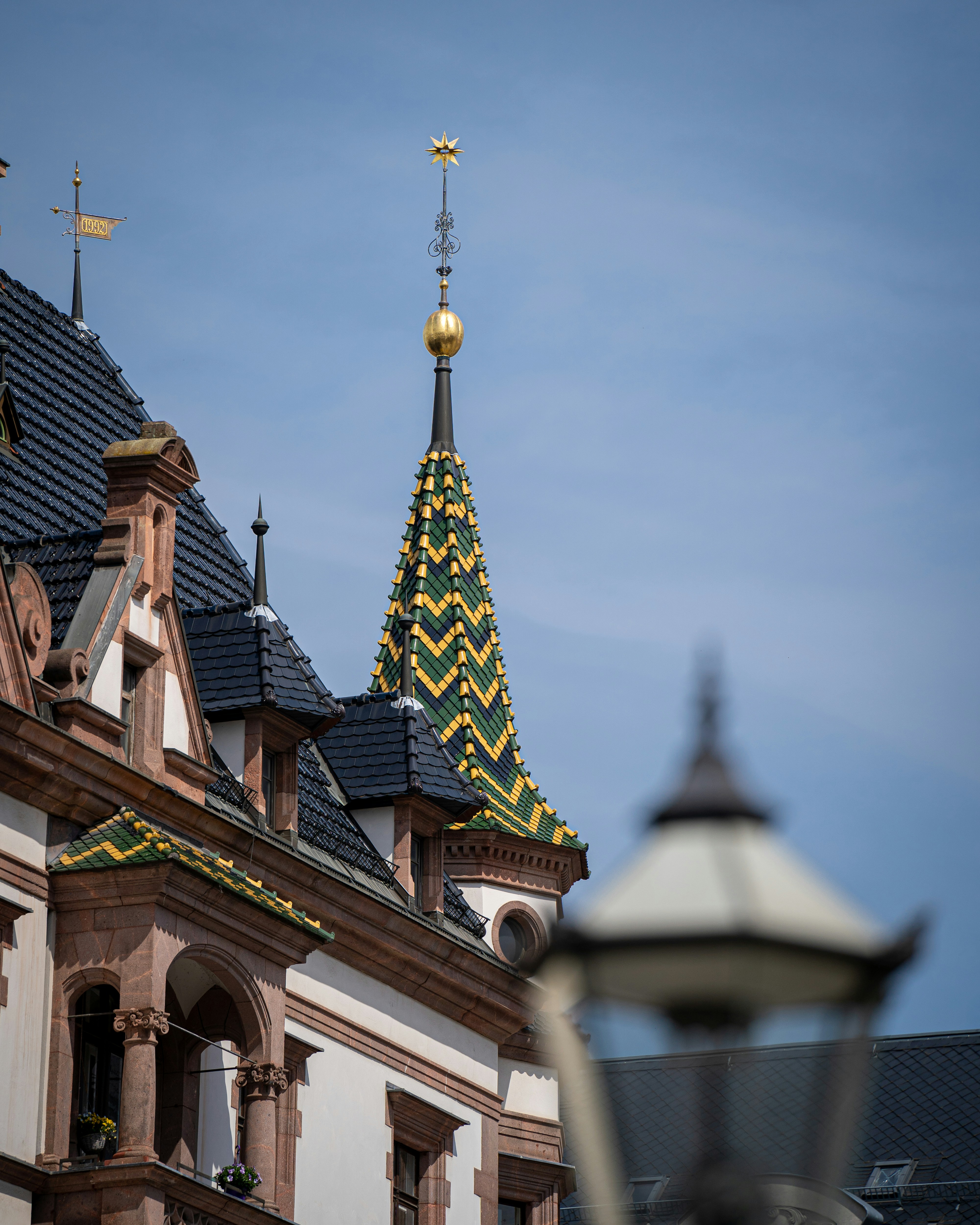 Crown of patterned tiles: a steep spire rises above a European facade
