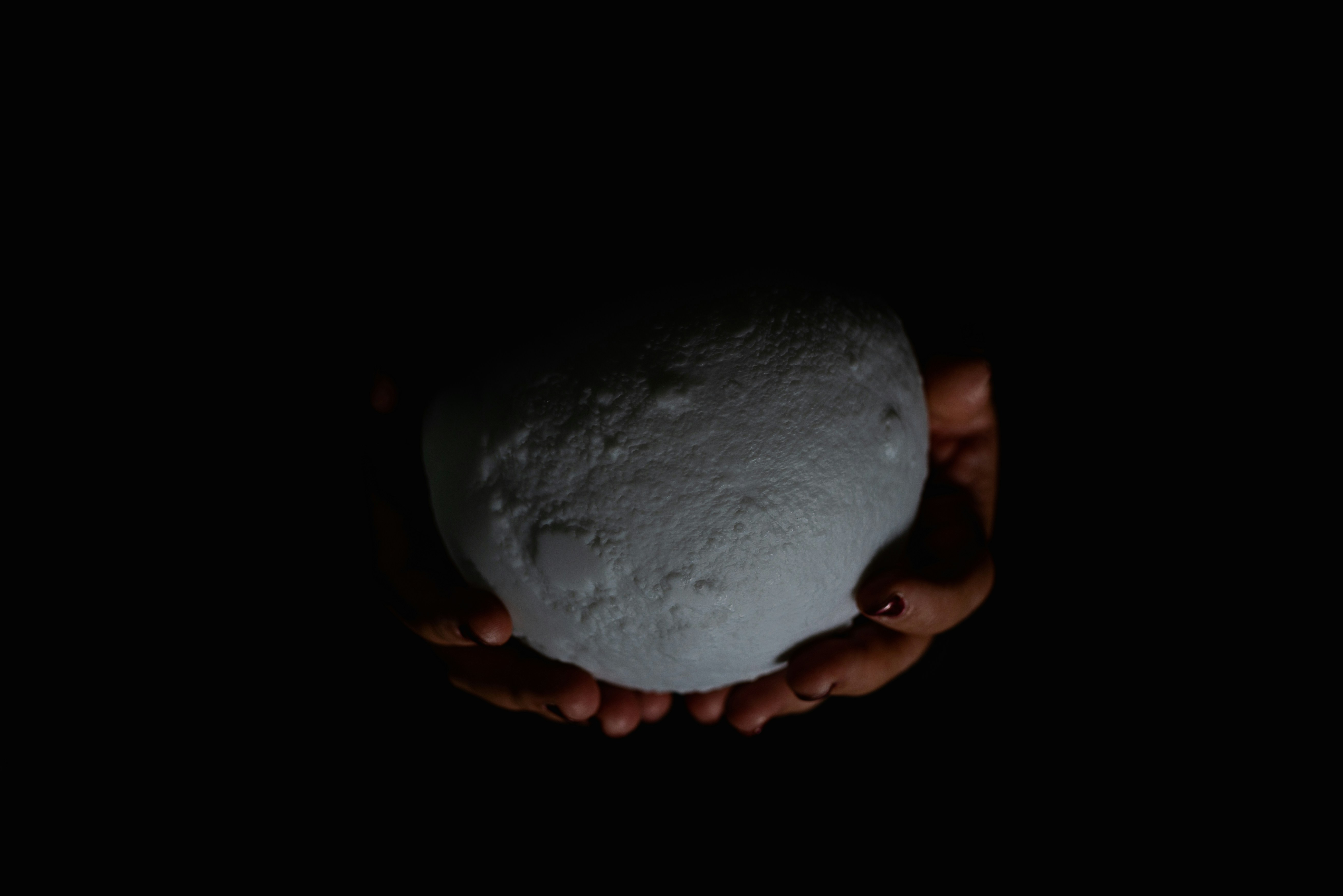Hands cradling a textured white sphere against a dark backdrop, evoking a sense of wonder and curiosity.