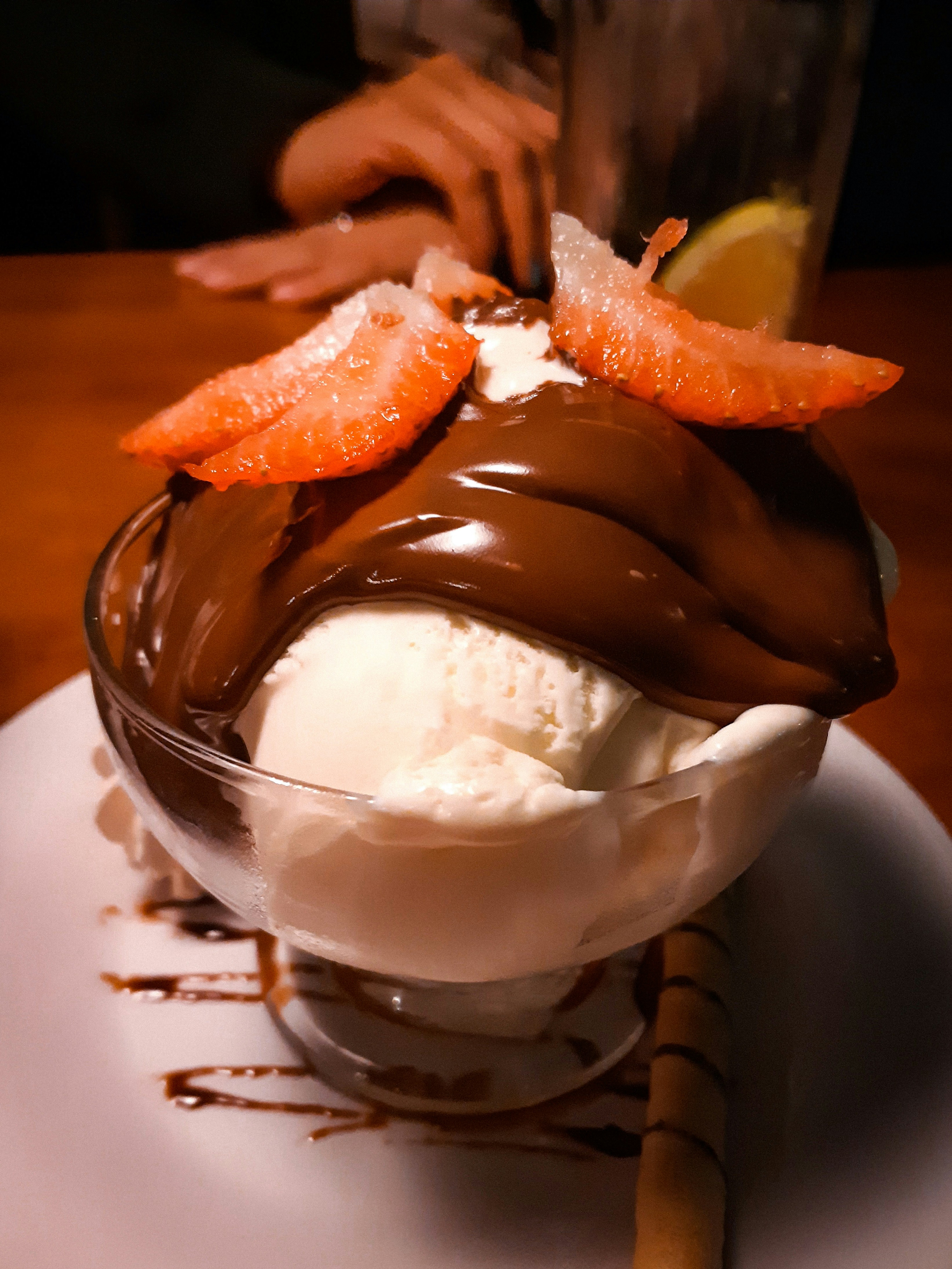 A luscious dessert featuring vanilla ice cream topped with rich chocolate sauce and fresh strawberries, served in a glass bowl.