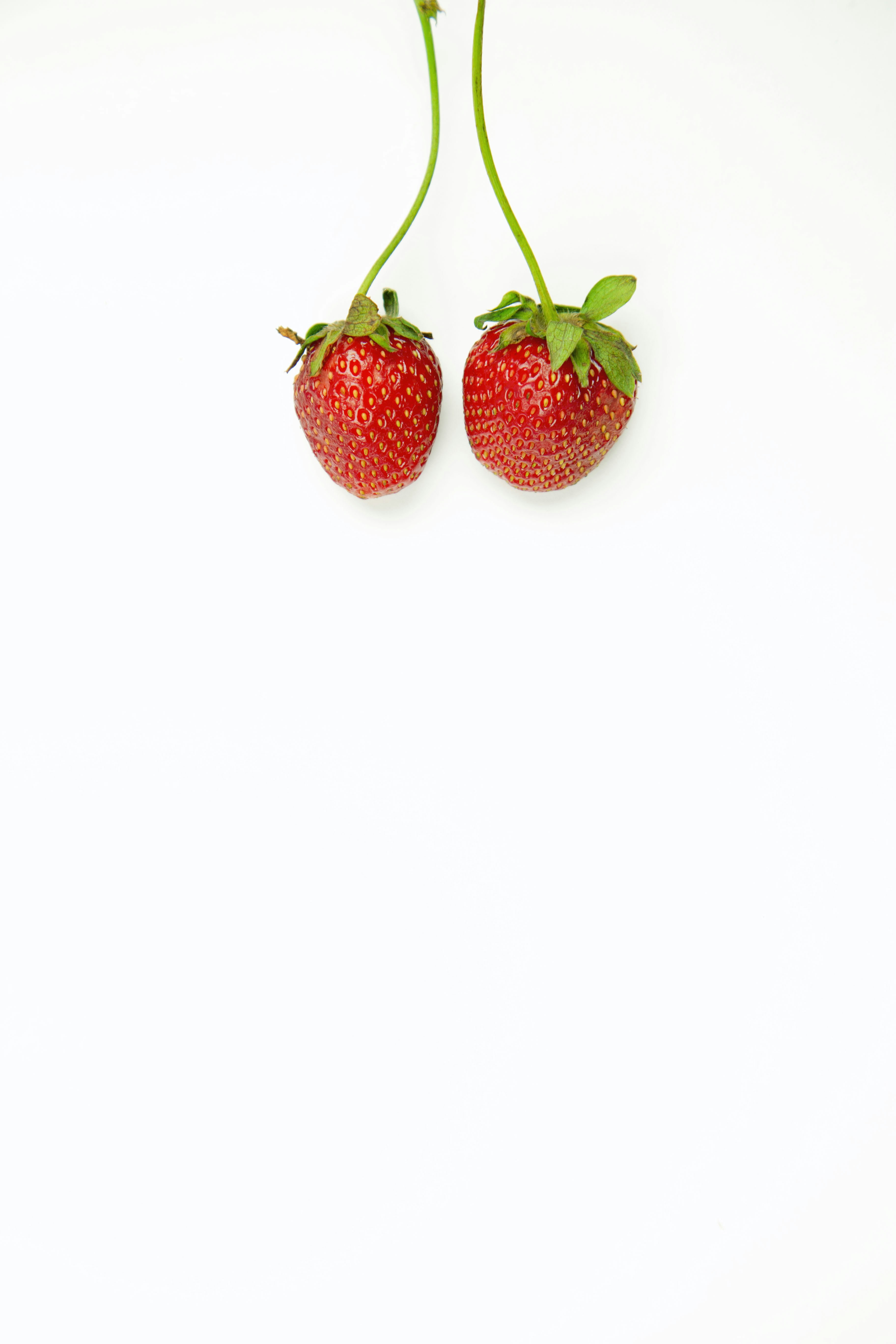 Twin strawberries suspended against a pristine white backdrop