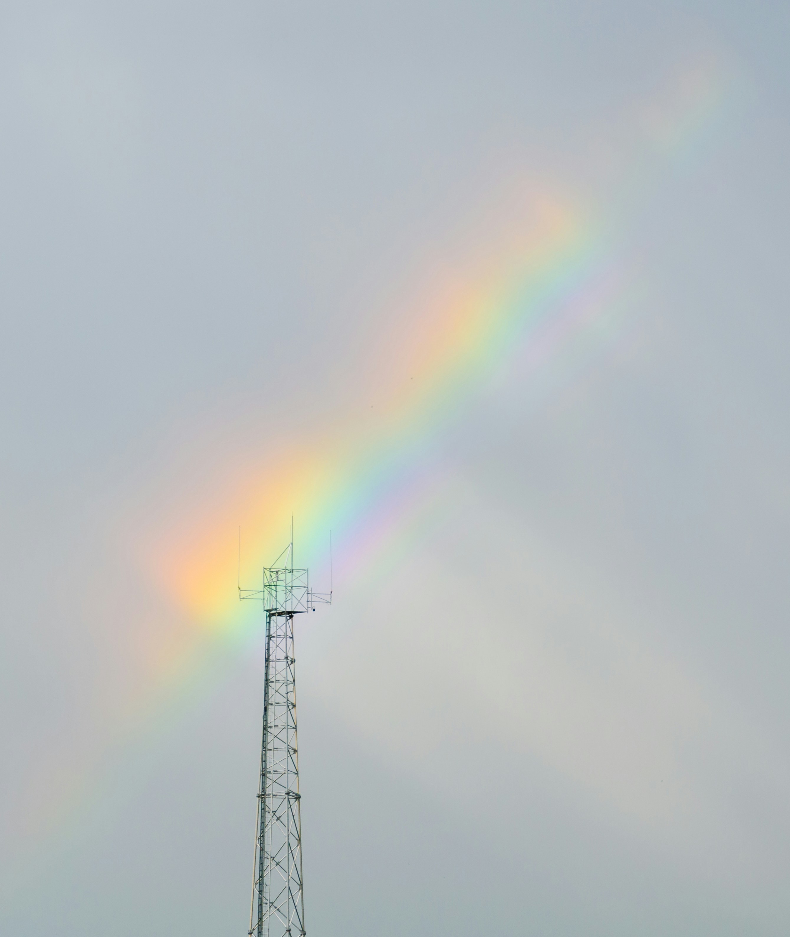 Chromatic Arc Behind a Transmission Tower in a Pale Sky