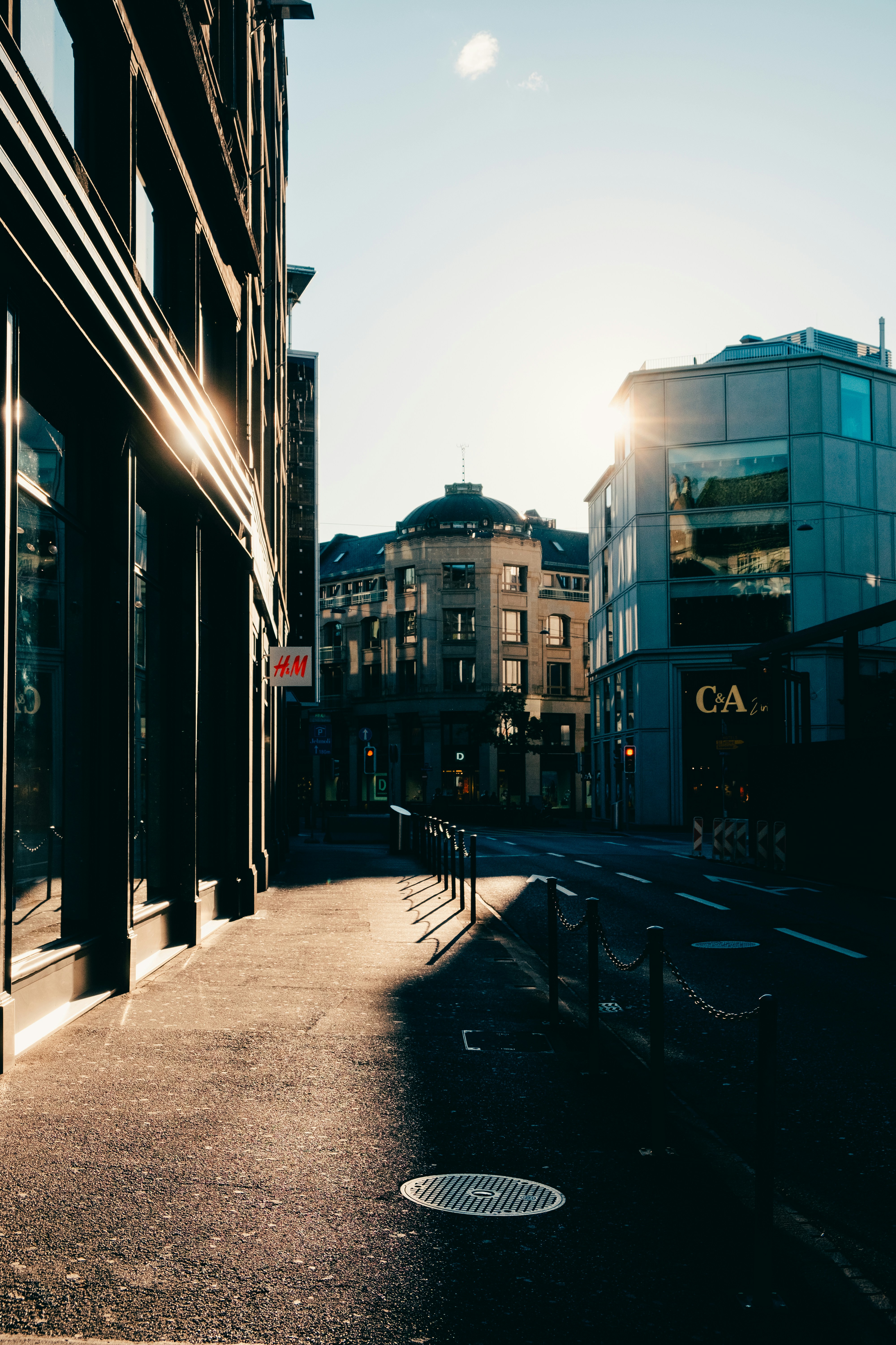 Sunlight casts long shadows on a city street, highlighting architectural details of nearby buildings. The scene captures the interplay of light and urban design.
