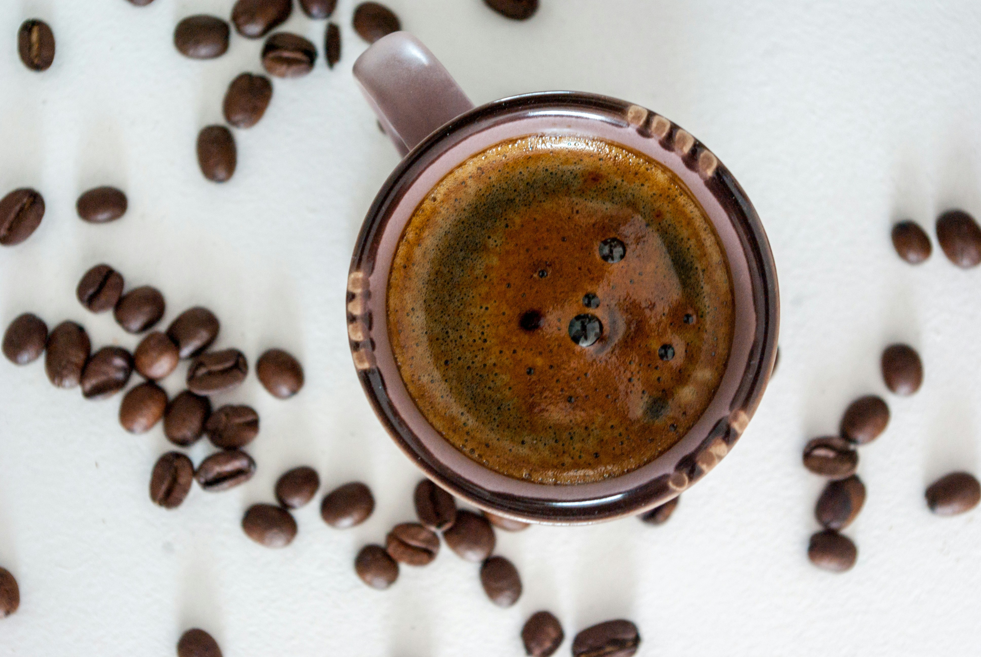 Close-up of a steaming cup of coffee surrounded by scattered coffee beans on a light background.