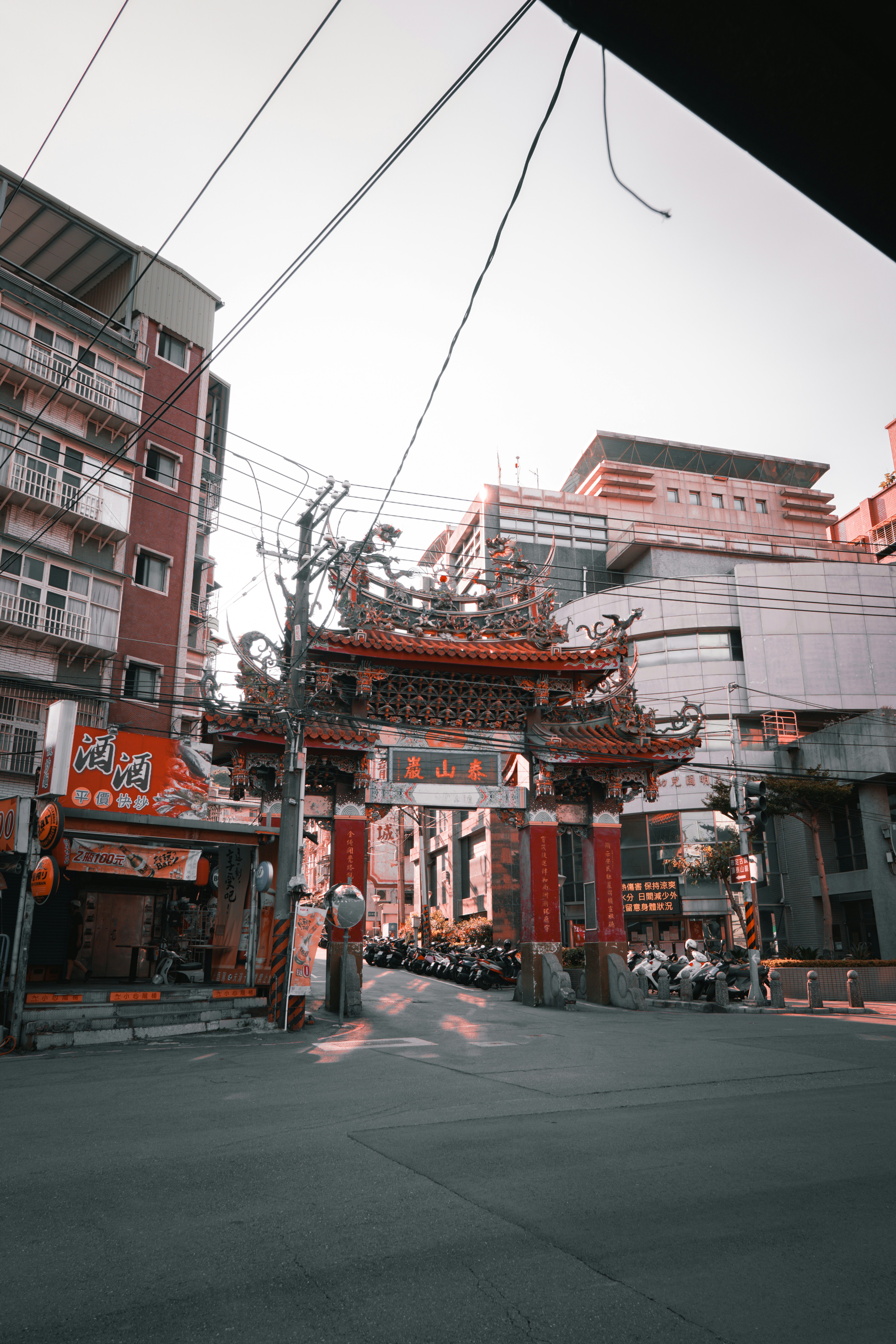 Intricately designed archway adorned with traditional motifs, marking the entrance to a vibrant street filled with local shops and motorbikes.