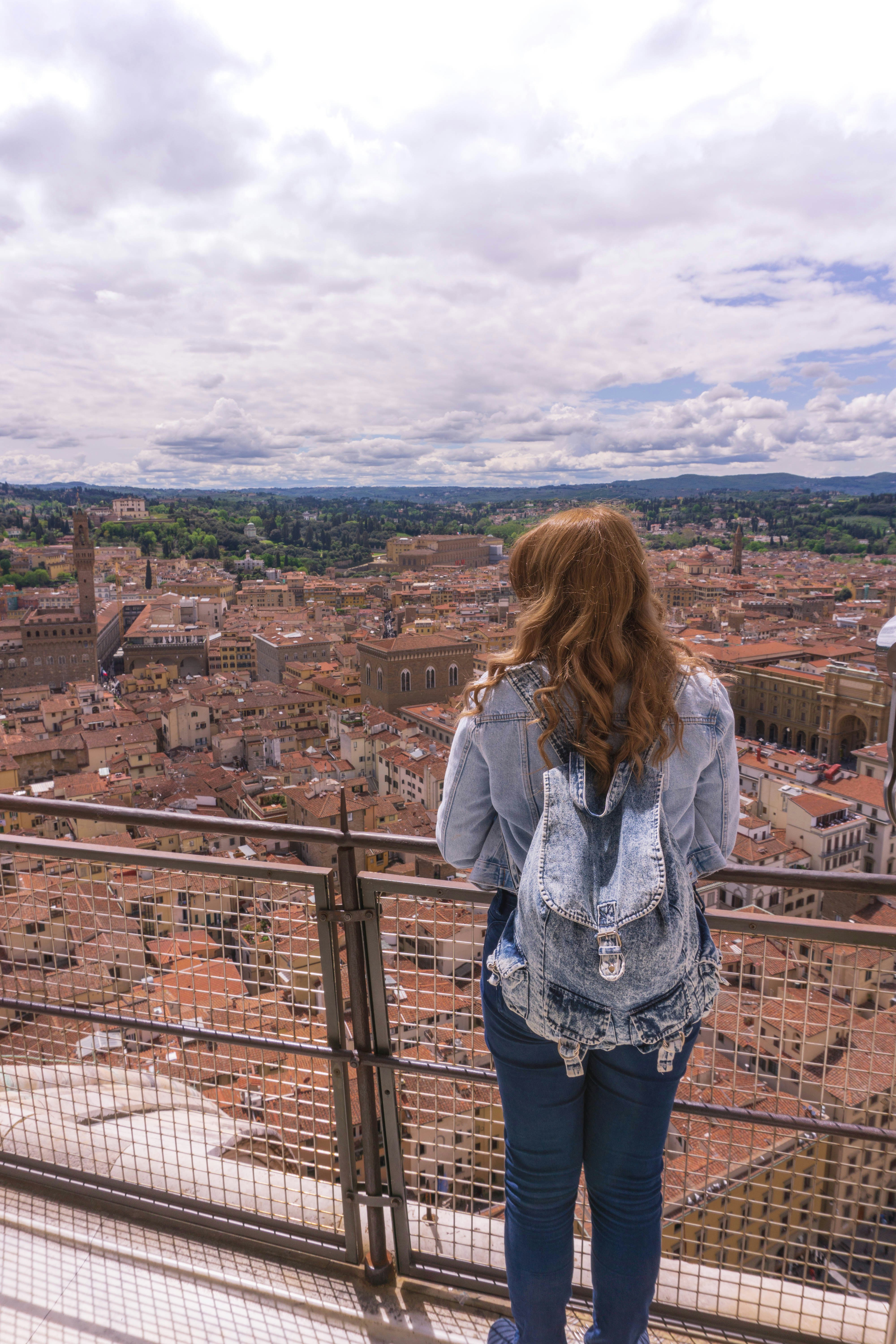A traveler gazes over the historic skyline of Florence, showcasing the city's iconic architecture and vibrant rooftops. The scene captures a moment of contemplation against a dramatic sky.