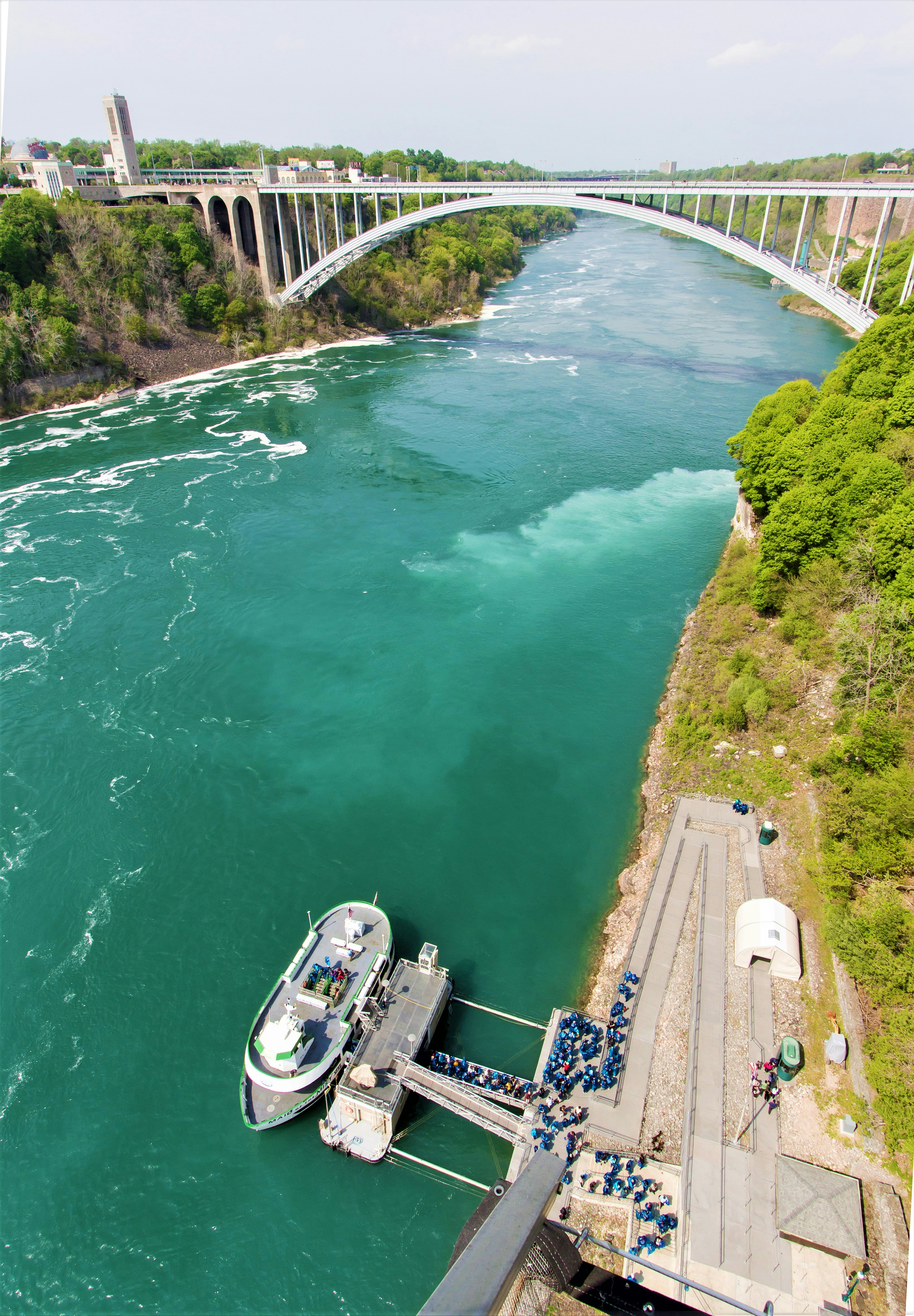 Aerial view of a river winding beneath a bridge, with a boat docked at a pier surrounded by lush greenery.