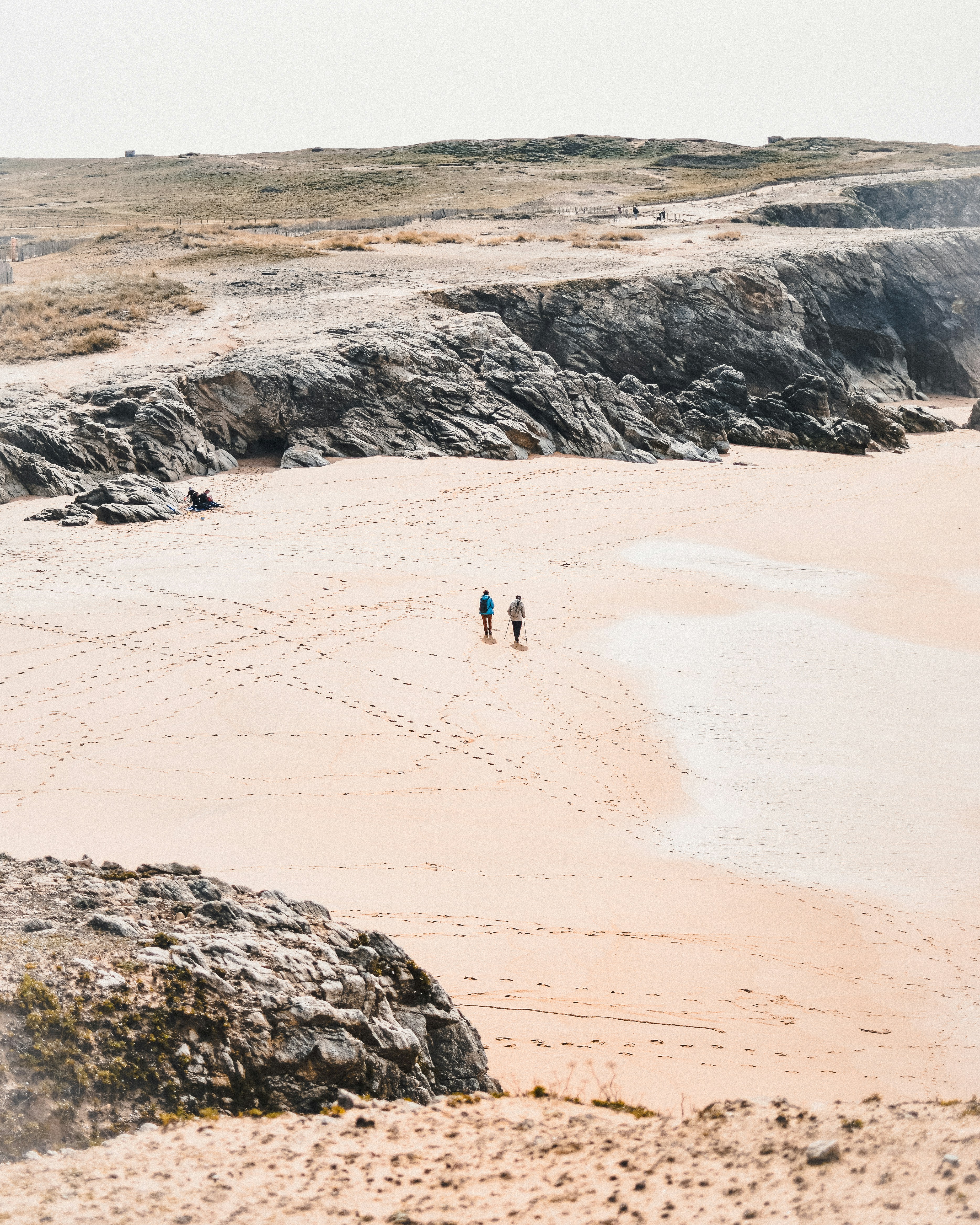 Two Figures on a Pale Beach: A Quiet Coastal Walk by Rugged Cliffs
