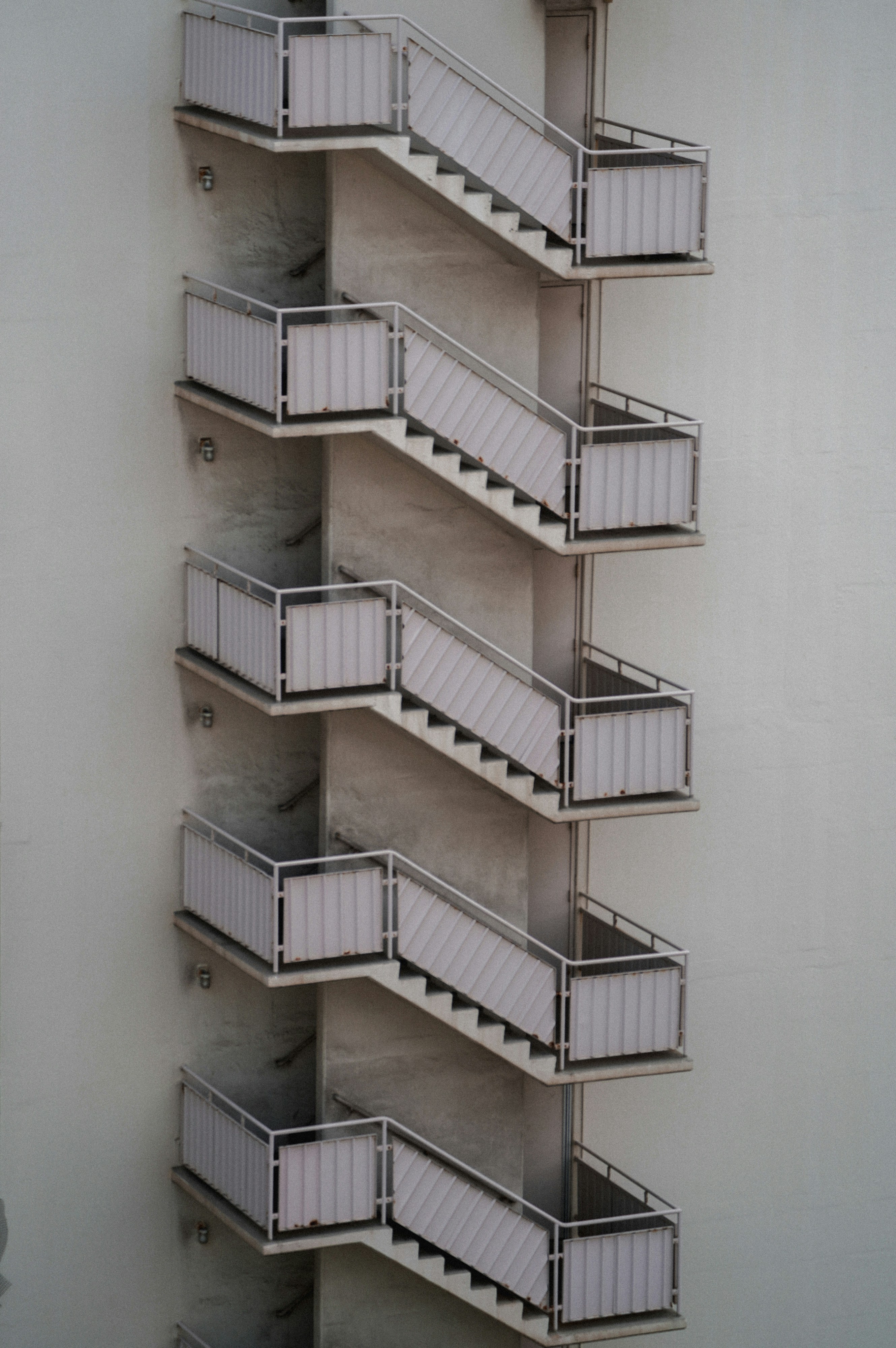 A vertical arrangement of fire escape stairs against a textured wall, showcasing geometric patterns and lines.