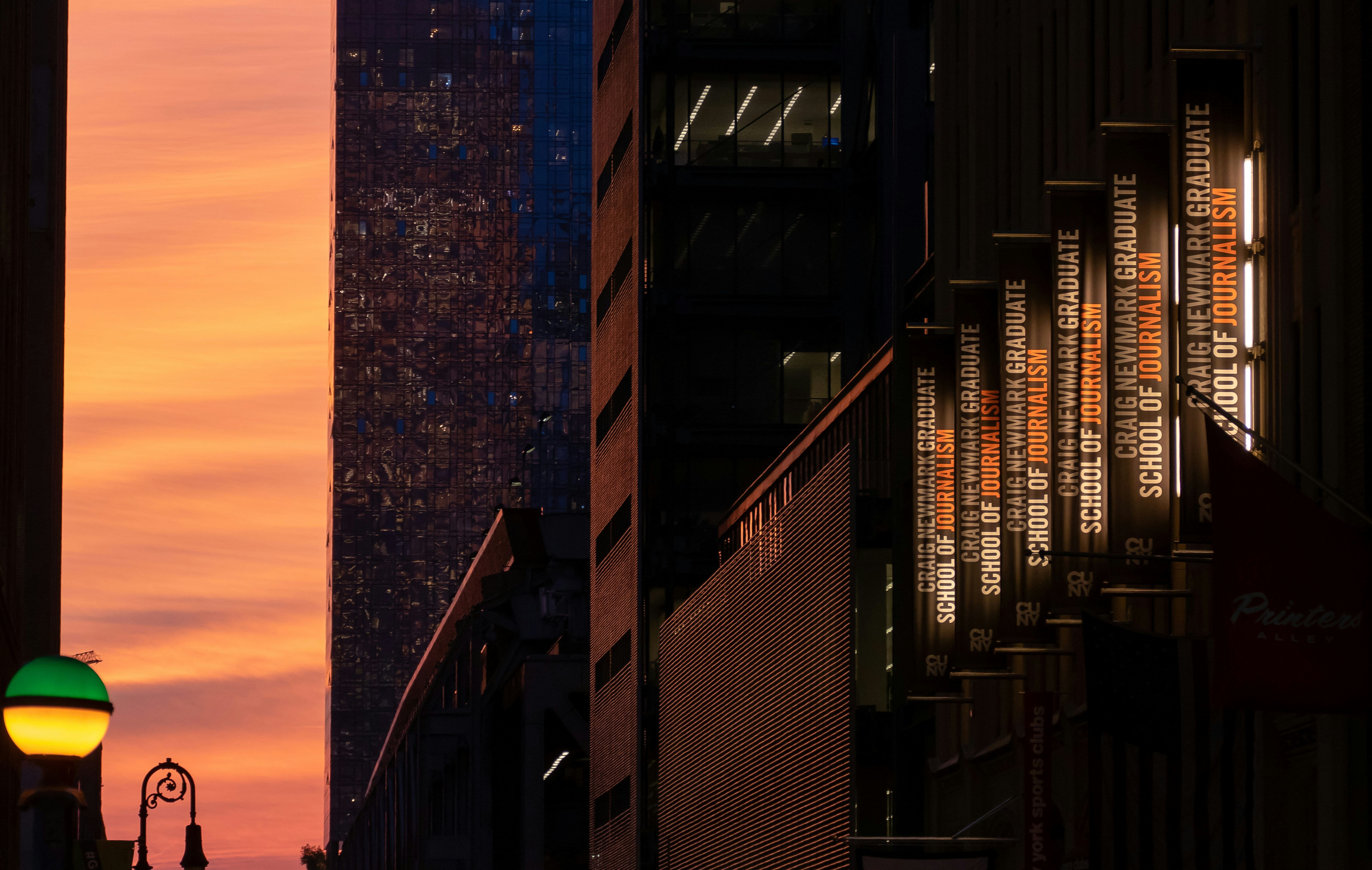 Vibrant sunset illuminating the skyline, with illuminated signage showcasing educational institutions along a city street.