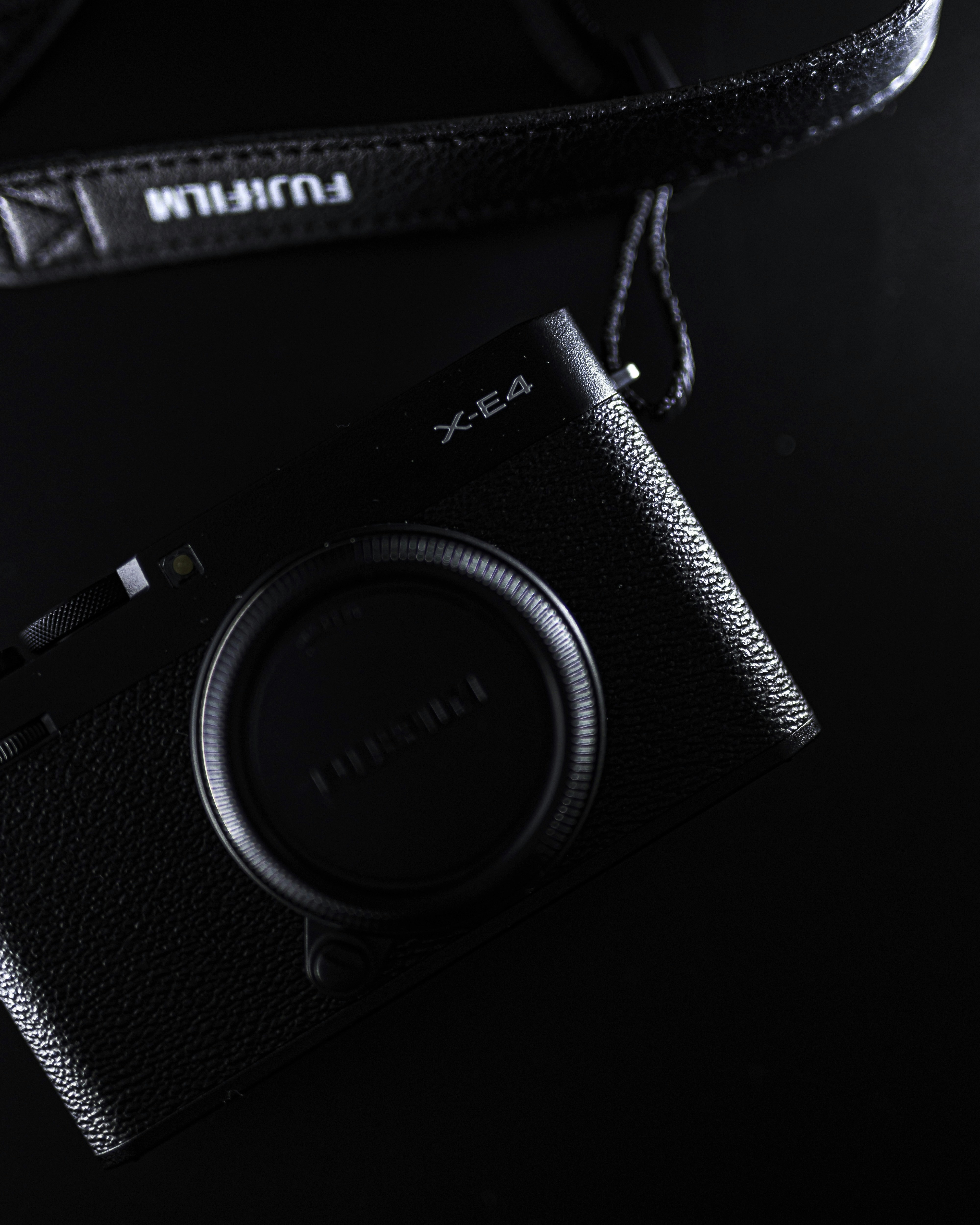 Fujifilm X-E4 camera resting against a dark backdrop, highlighting its sleek design and textured surface.