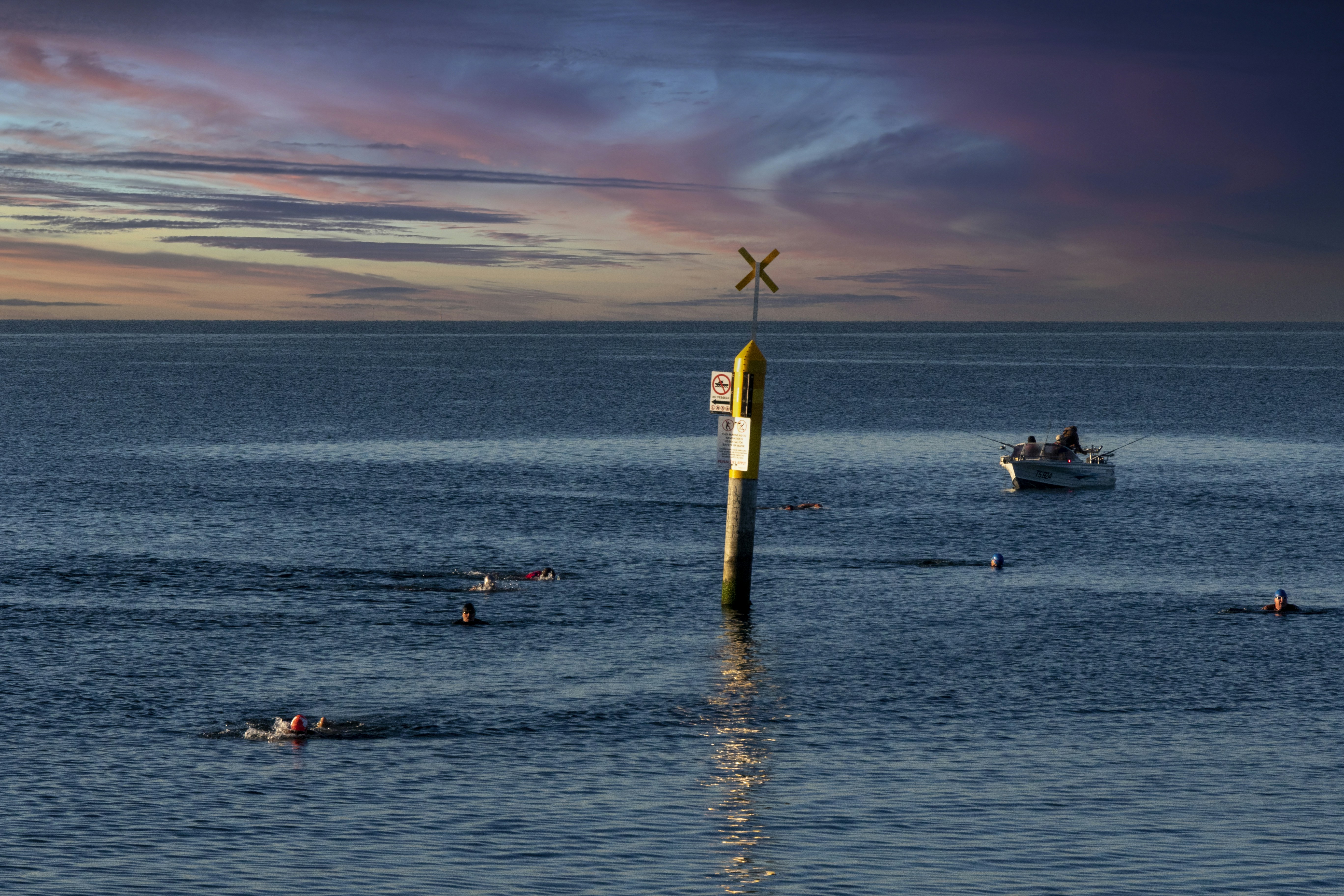 Marker in the Calm Gulf: Lone Beacon and Passing Boats at Dusk