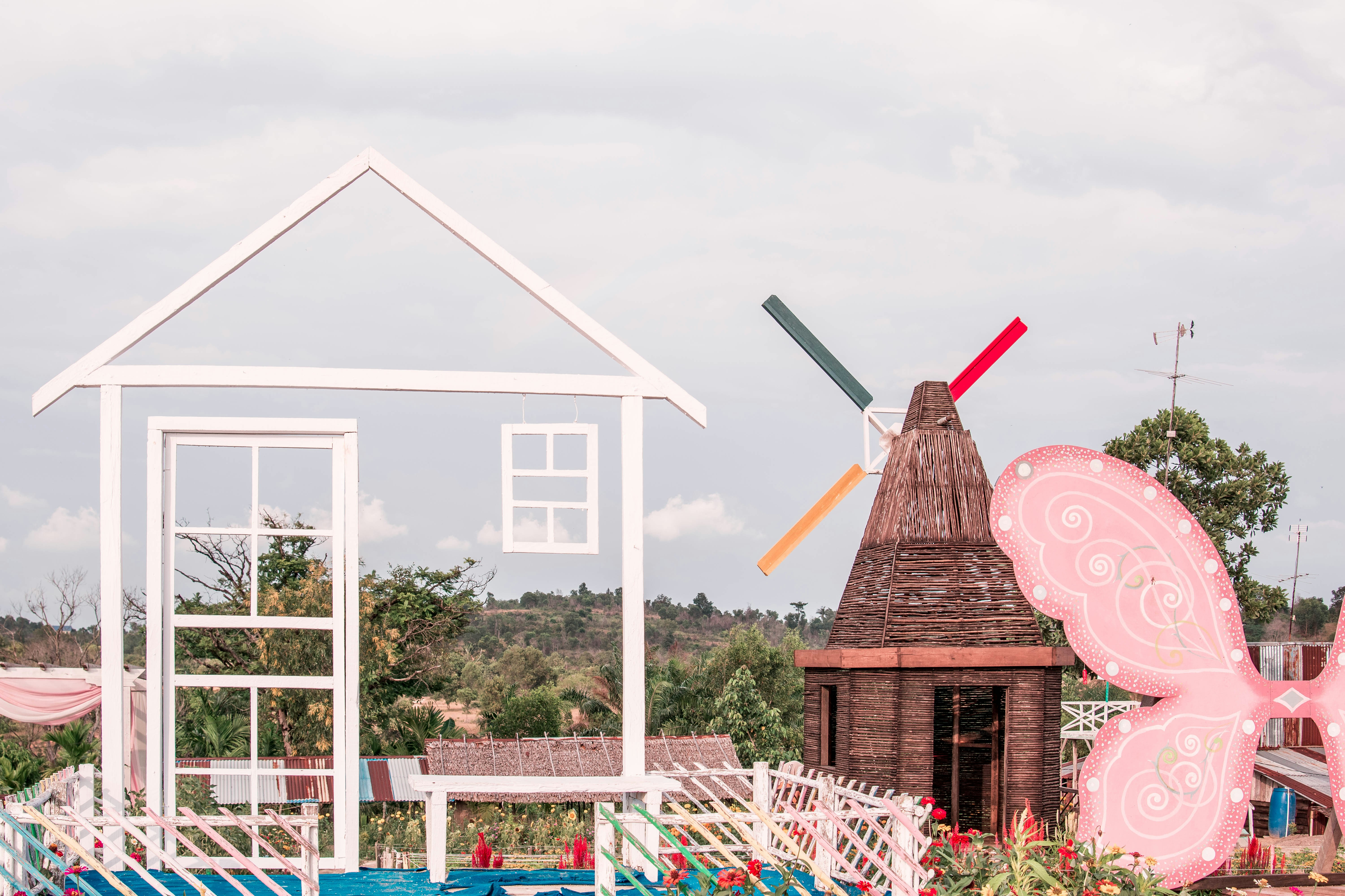 White house frame and colorful windmill in a garden setting under a cloudy sky.