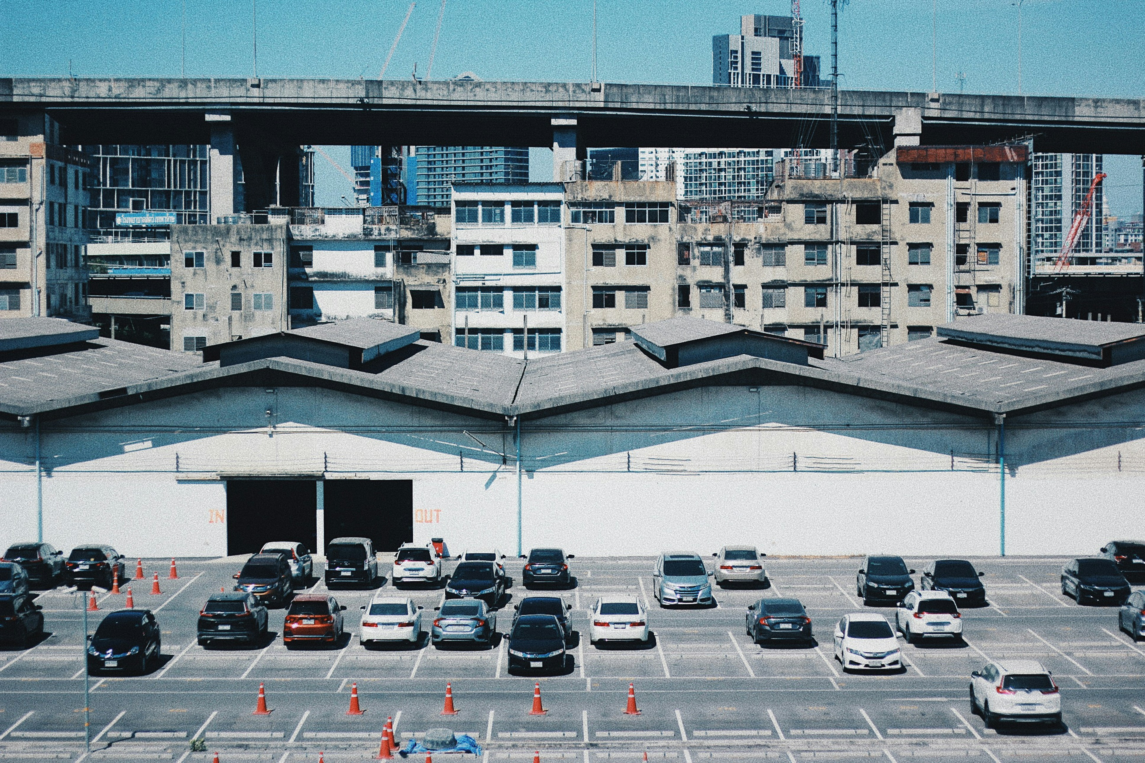 Abandoned industrial buildings juxtaposed with an active parking lot beneath a highway overpass.