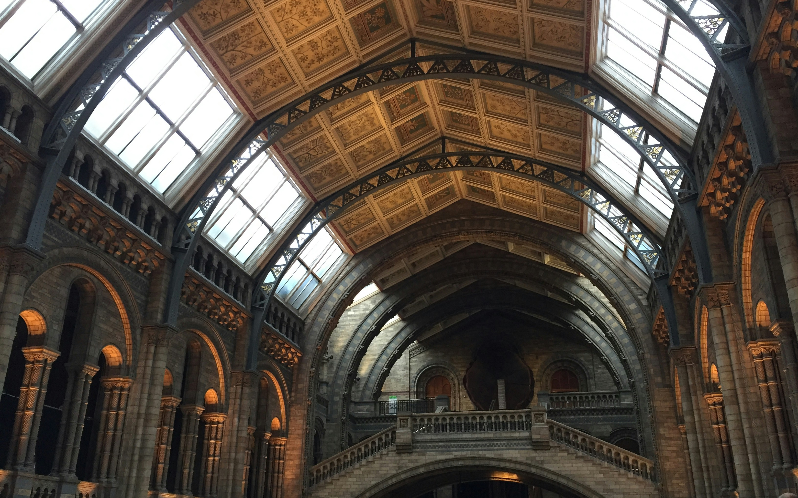 Intricate vaulted ceiling of a historic museum, showcasing elaborate architectural details and natural light filtering through large windows.