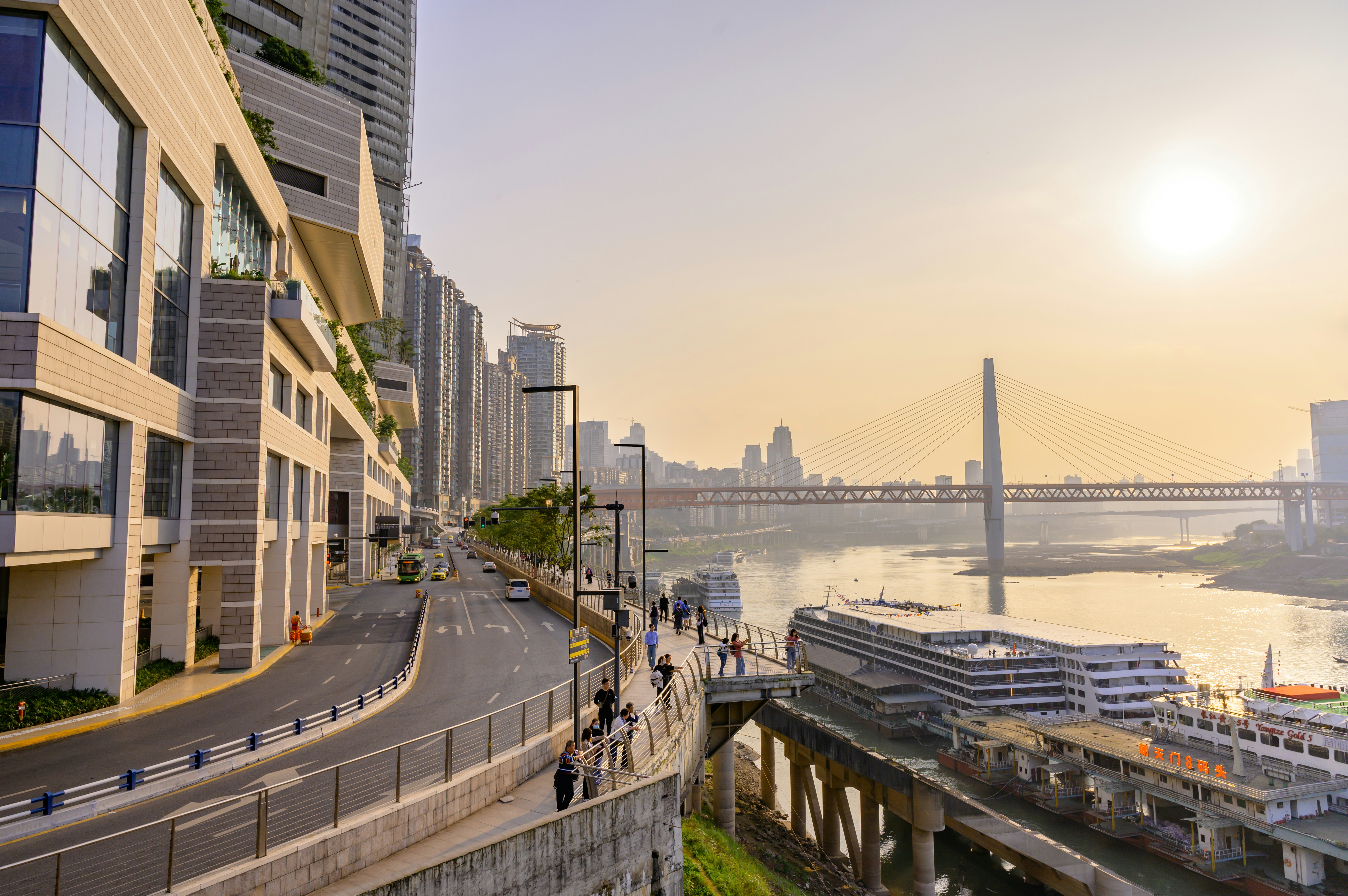 Modern cityscape with a riverside promenade under the warm morning sun.
