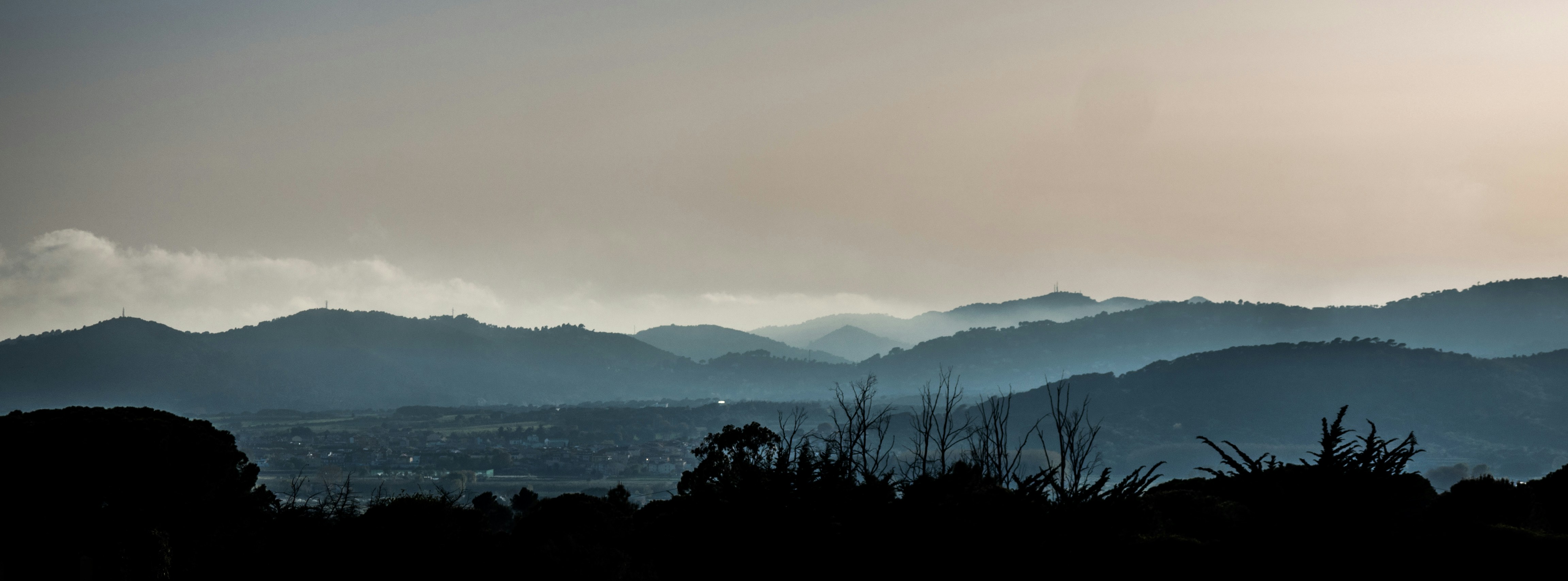 Silhouetted trees frame distant mountains under a softly lit sky.