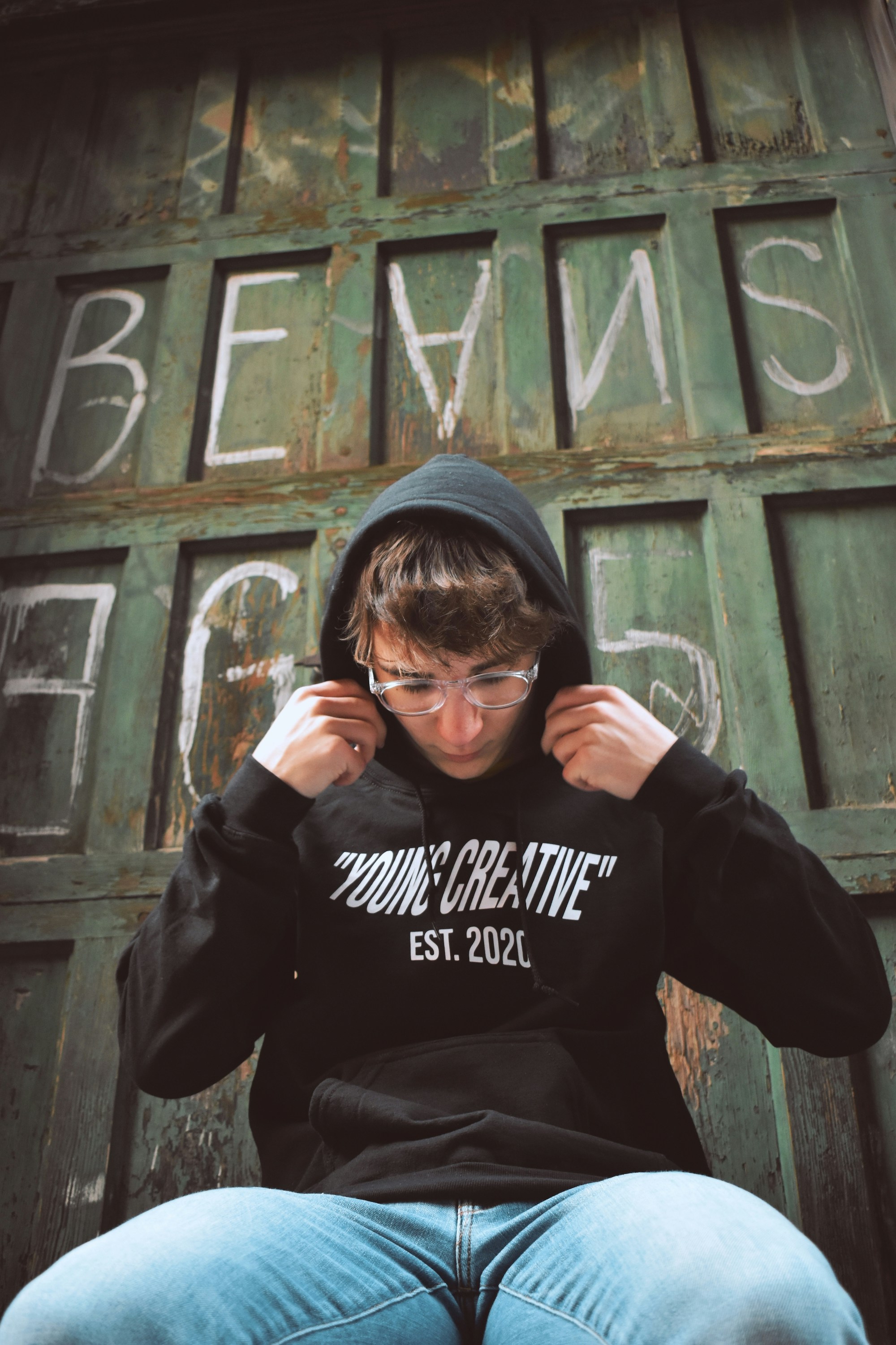 Hooded focus: a quiet study of youth beneath weathered green panels