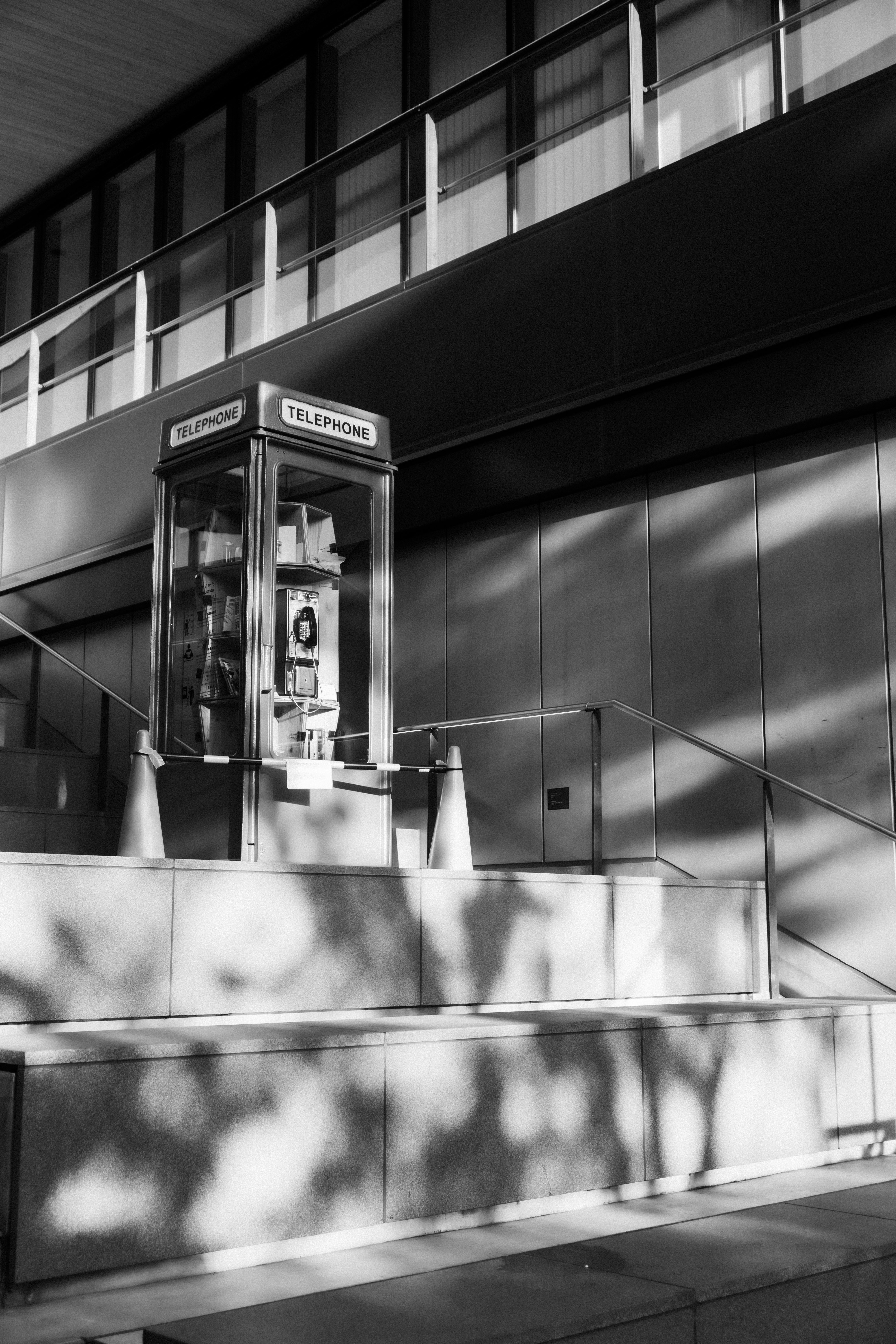 Retro Telephone Booth Standing Guard Among Concrete Lines and Shifting Shadows