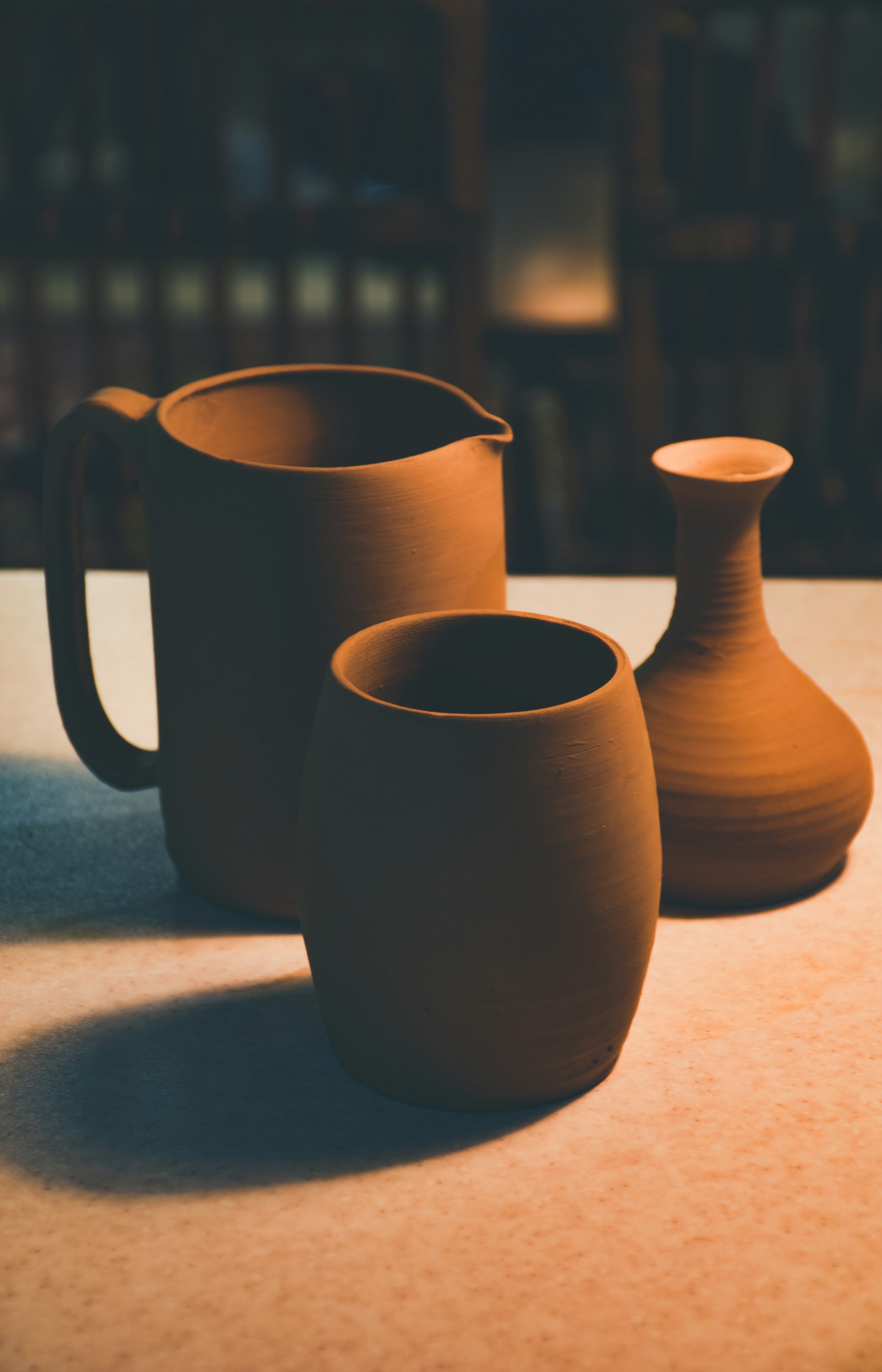 Three handcrafted clay vessels with varying shapes and sizes, illuminated softly to highlight their textures and contours.