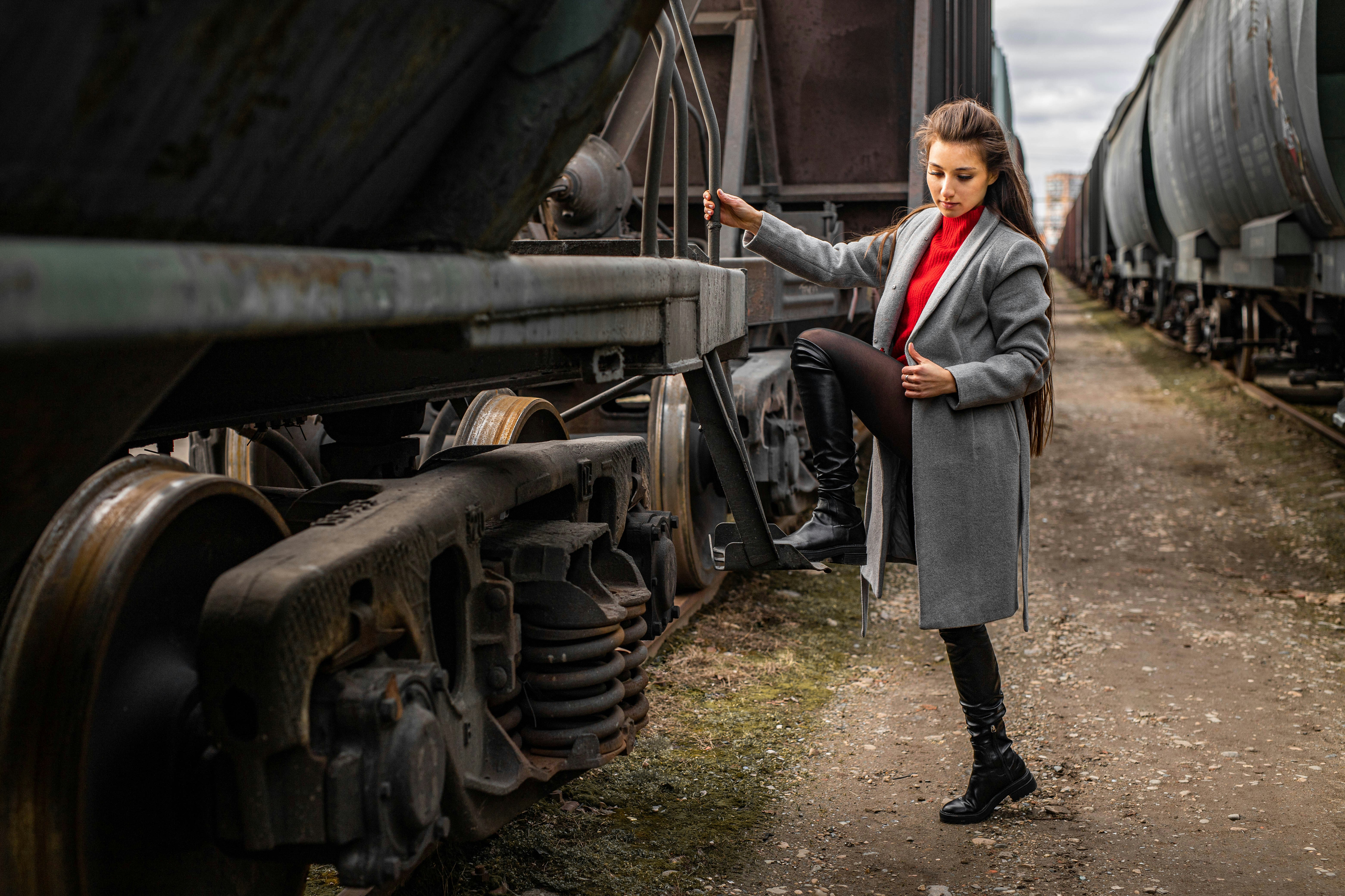 woman in gray coat standing beside train during daytime