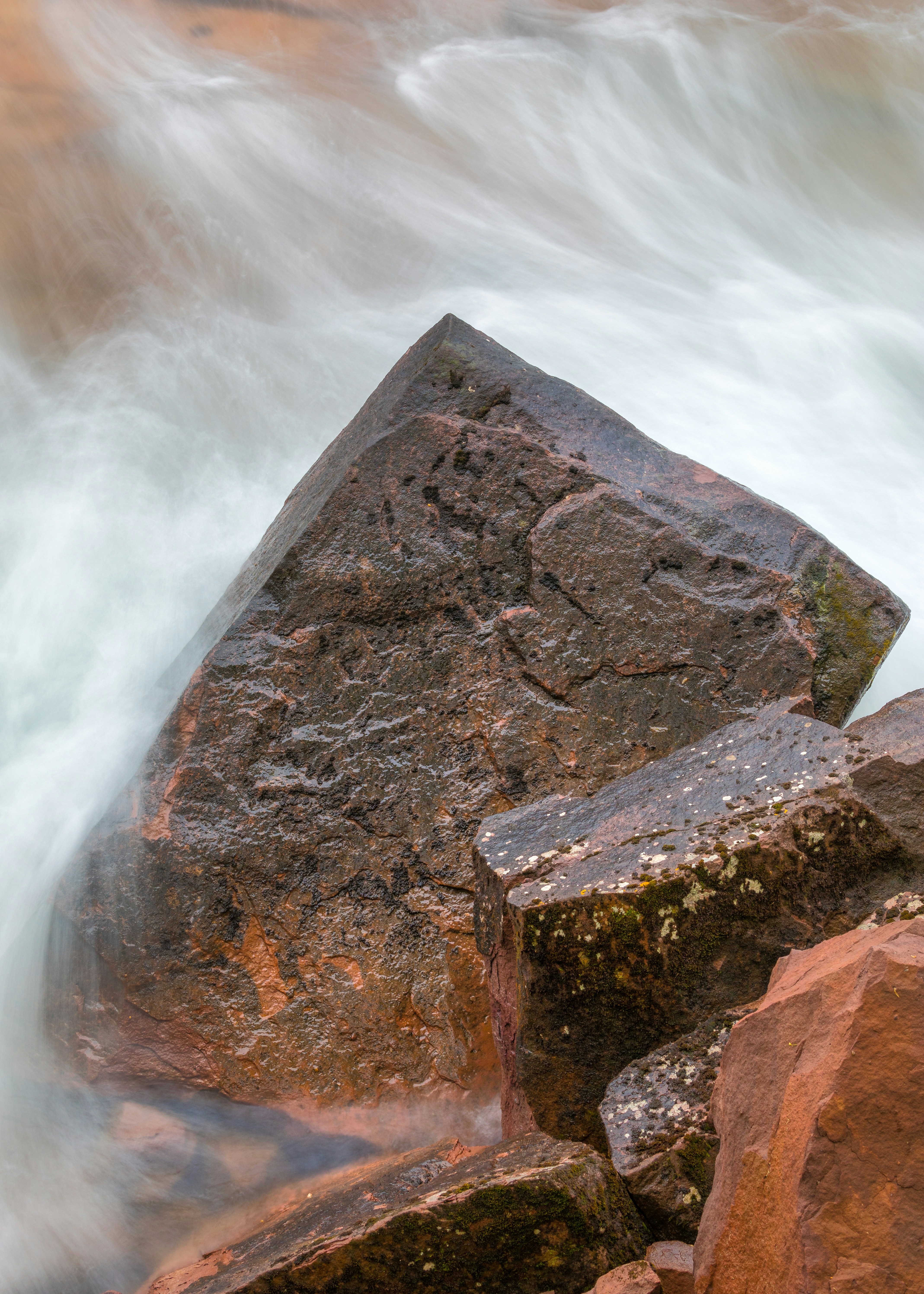 Moss-covered rocks partially submerged as a stream flows swiftly around them.