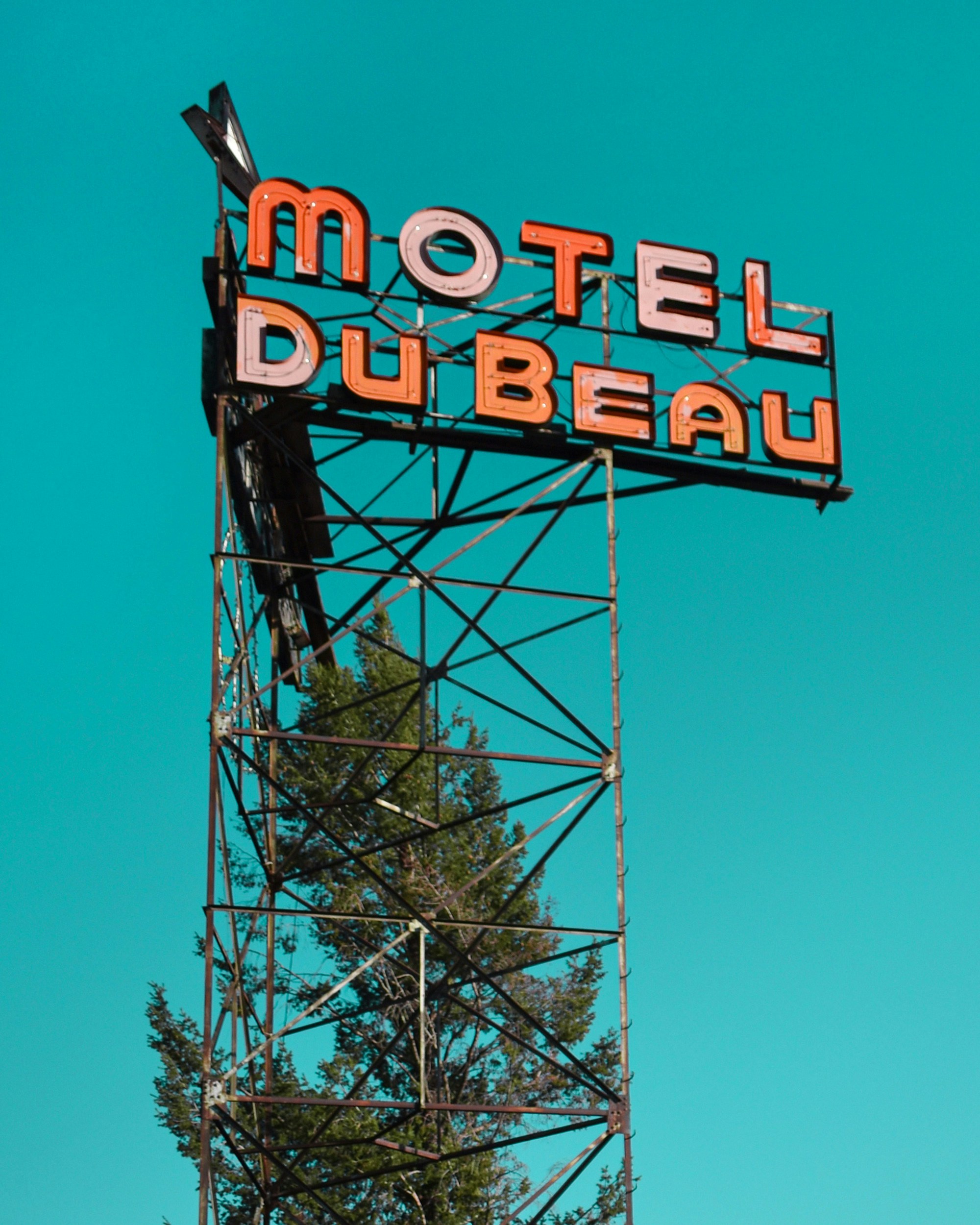 Teal Sky Neon: Motel Dubeau Sign on a Lattice Tower