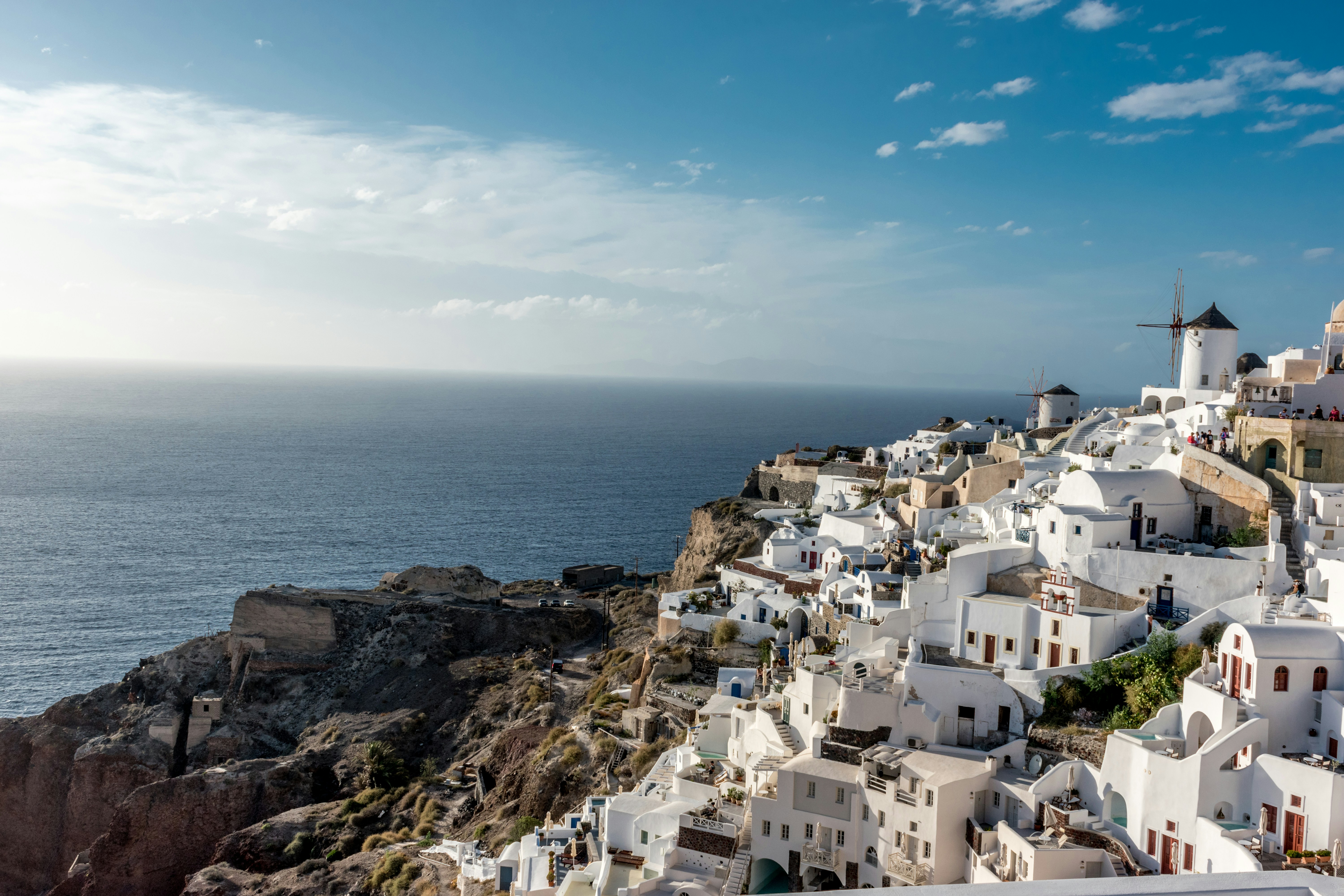 Whitewashed buildings perched on a cliff overlooking the Aegean Sea under a clear blue sky.