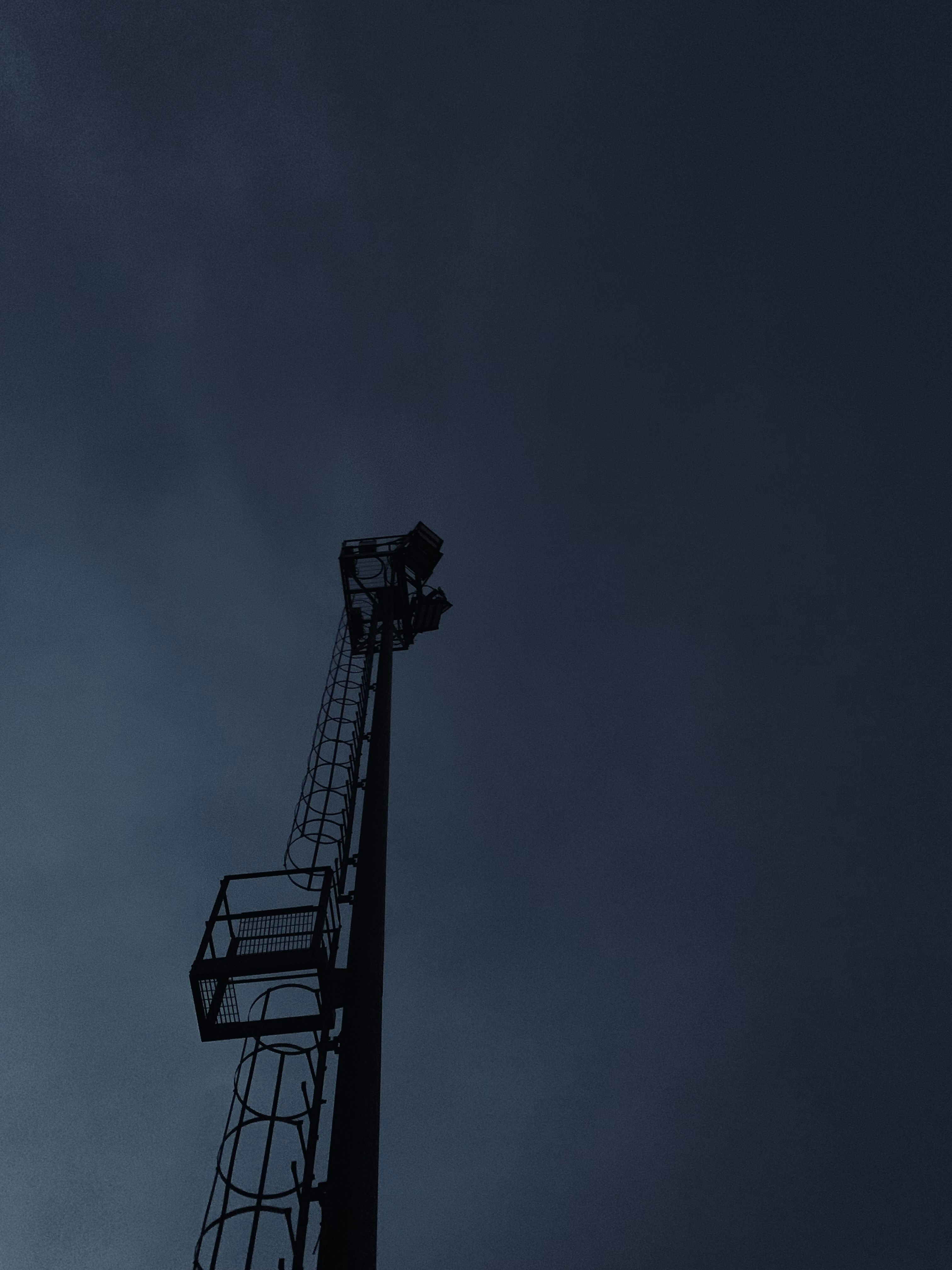 Twilight Sentinel: silhouette of a lone floodlight mast against a velvet dusk sky