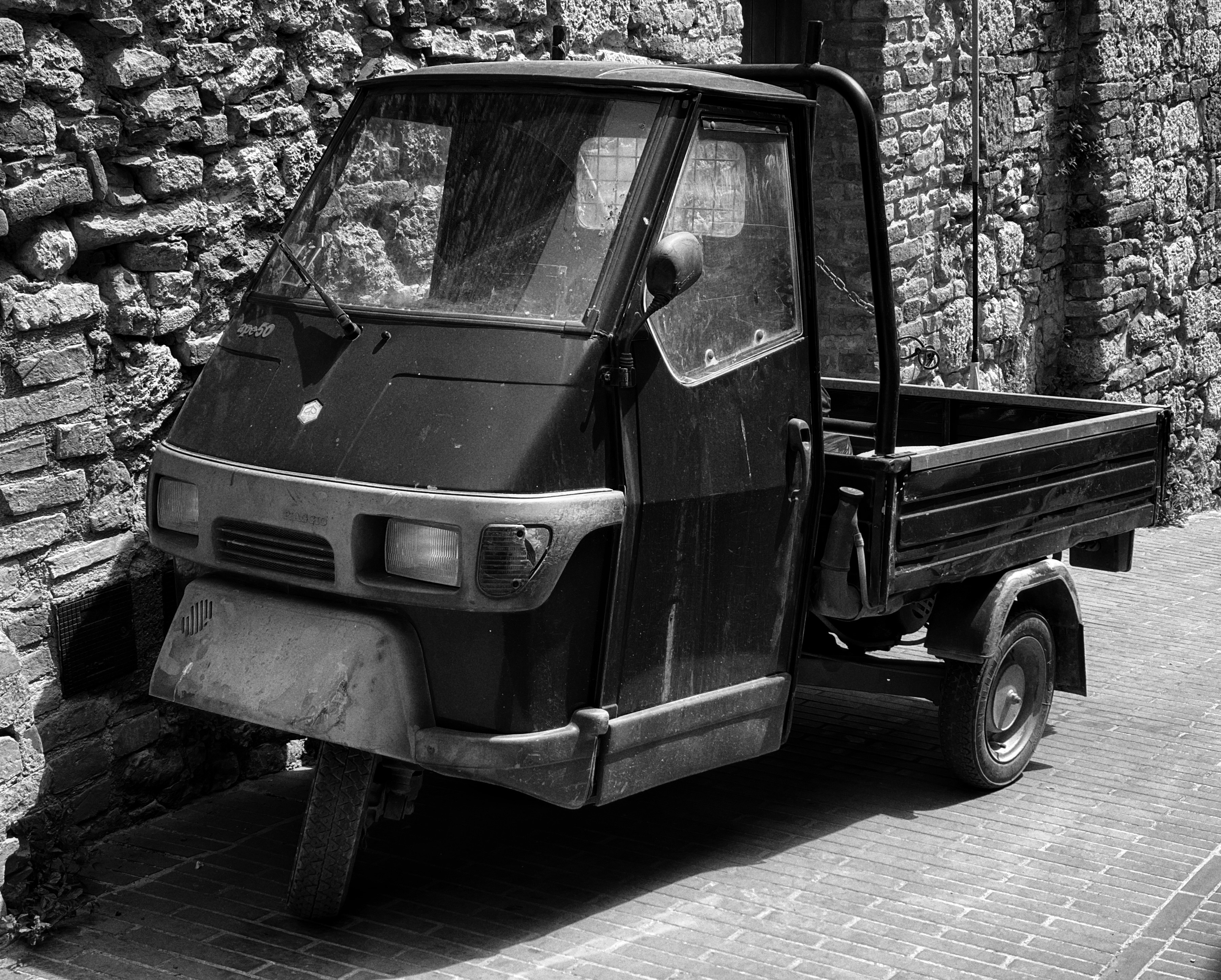 A weathered tuktuk rests against a textured stone wall, showcasing its vintage charm and urban character.