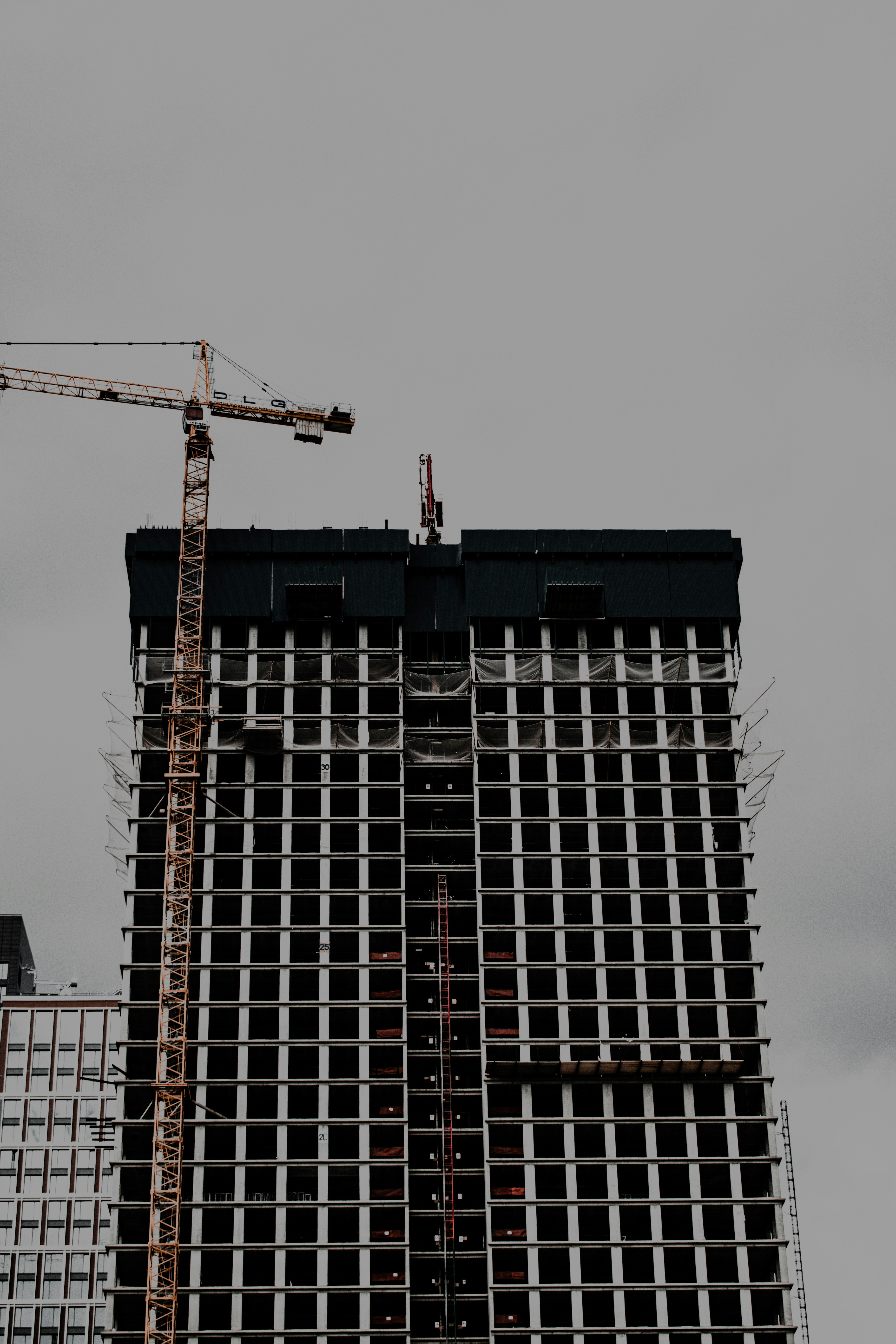 Construction site of a high-rise building featuring a prominent crane against a cloudy sky.