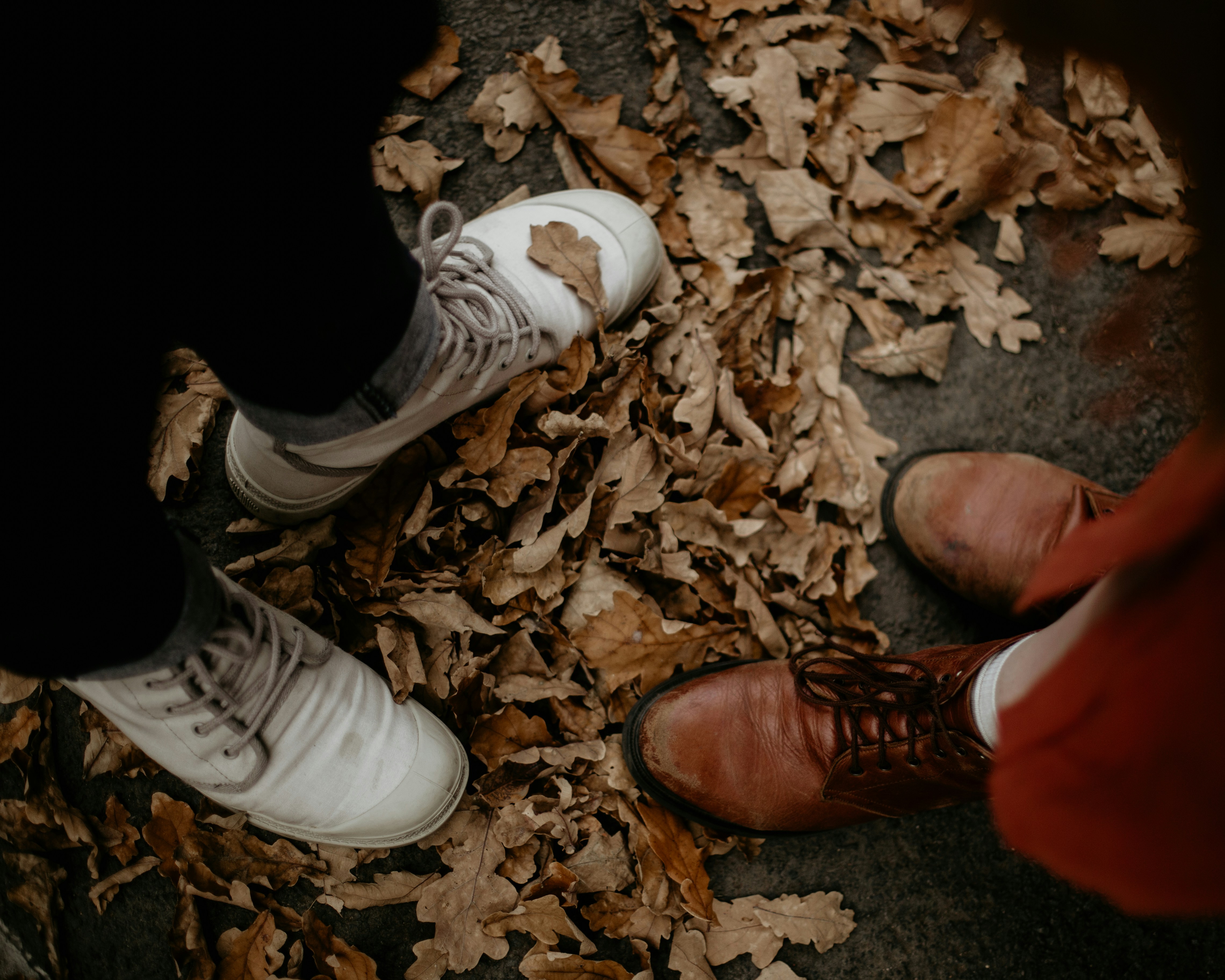 Autumn Footfall: White Sneakers Meet Brown Boots on a Leaf-Littered Path
