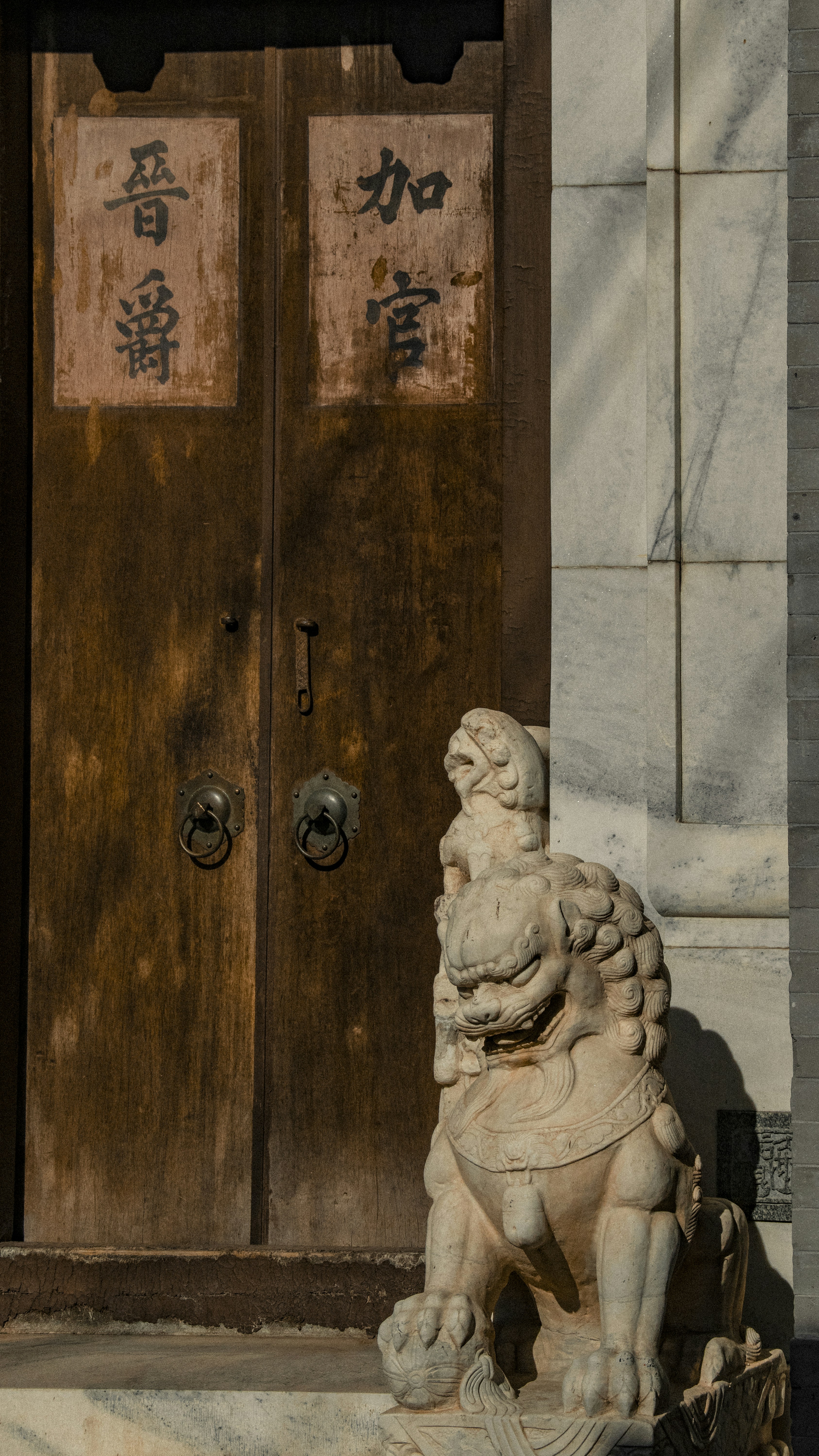 Stone lion statue guarding a weathered wooden door adorned with traditional inscriptions.
