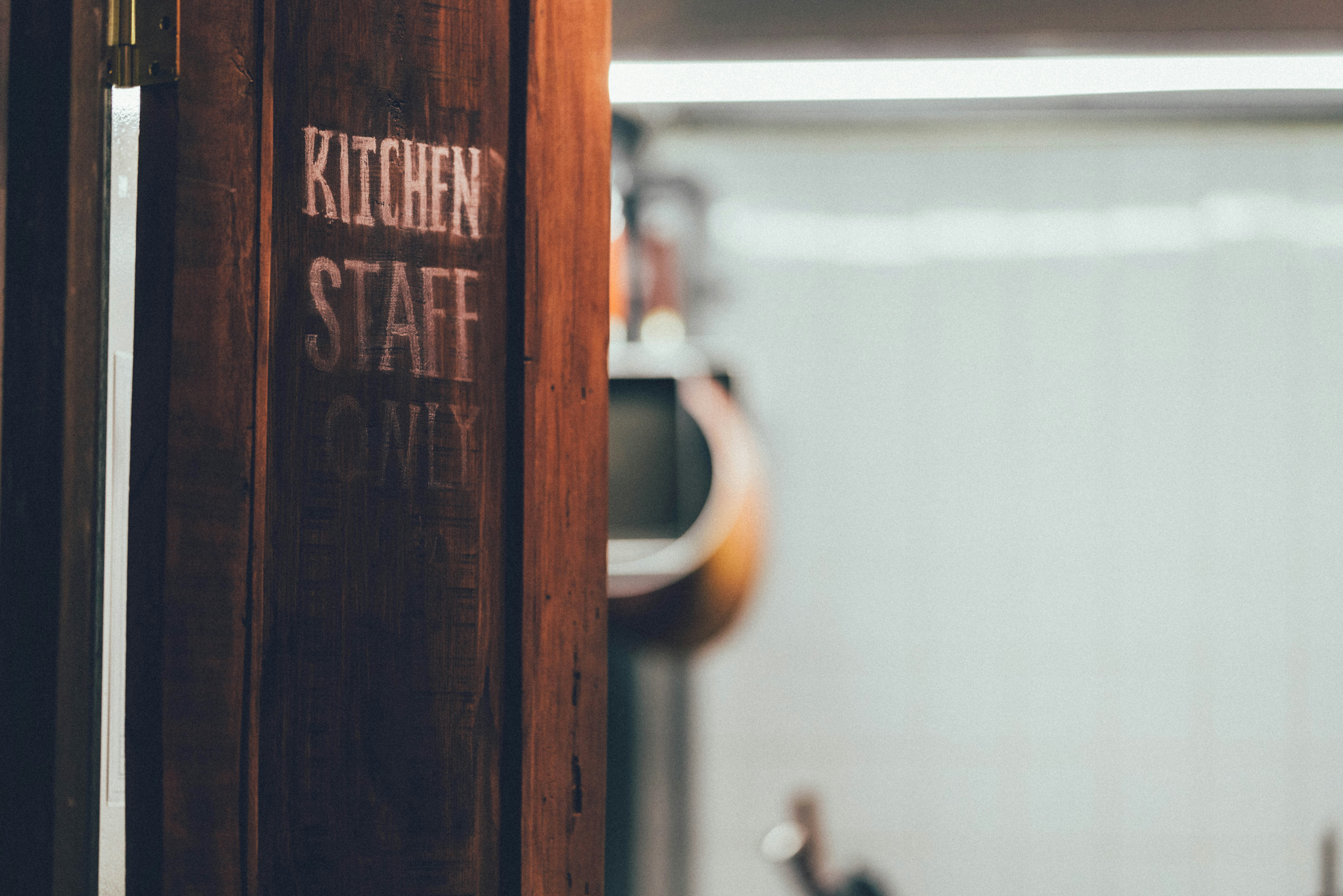 Wooden door with 'KITCHEN STAFF ONLY' sign, leading to a bustling kitchen environment.