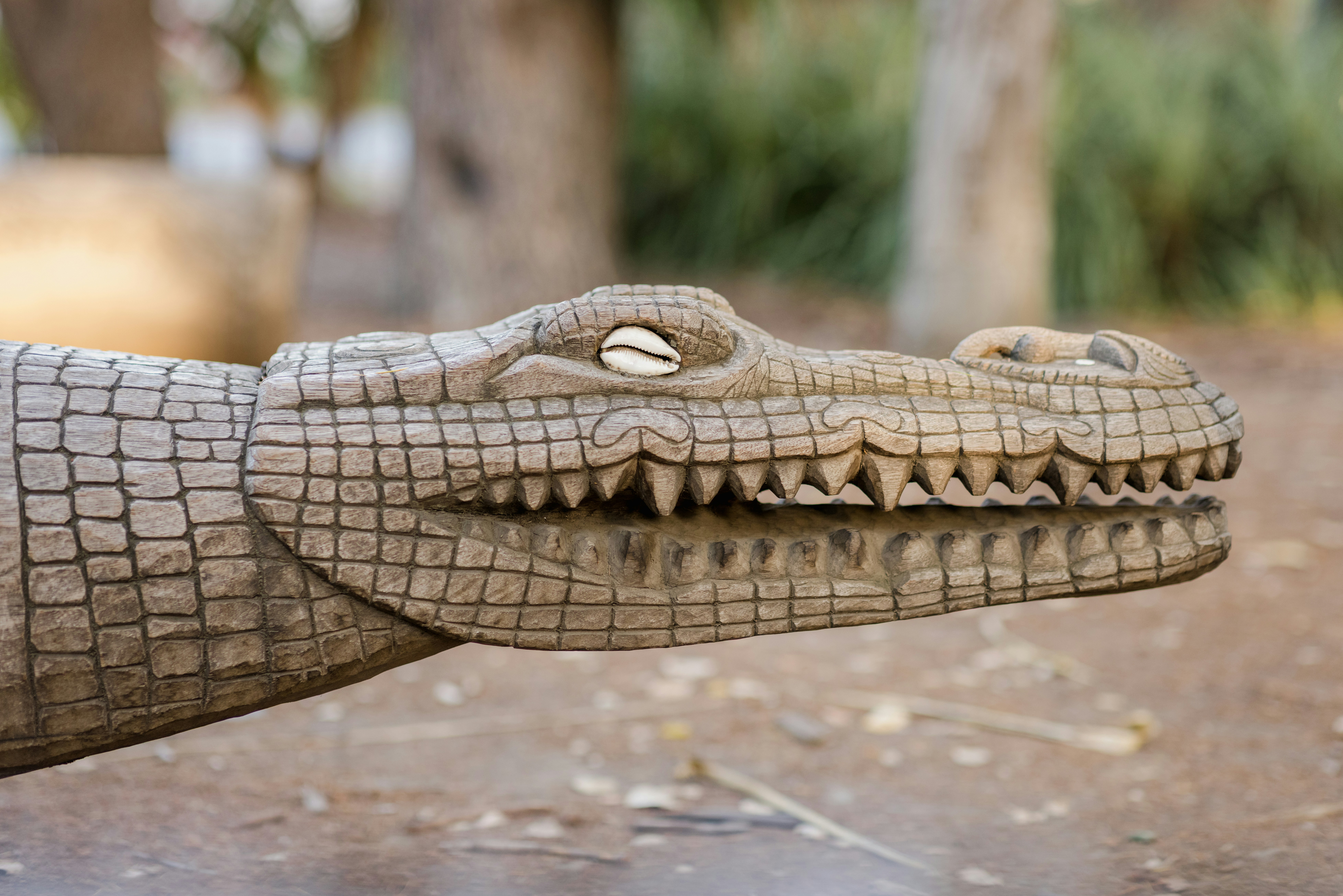 Intricately carved wooden alligator head showcasing detailed scales and fierce expression. The artwork captures the essence of the reptile's character.
