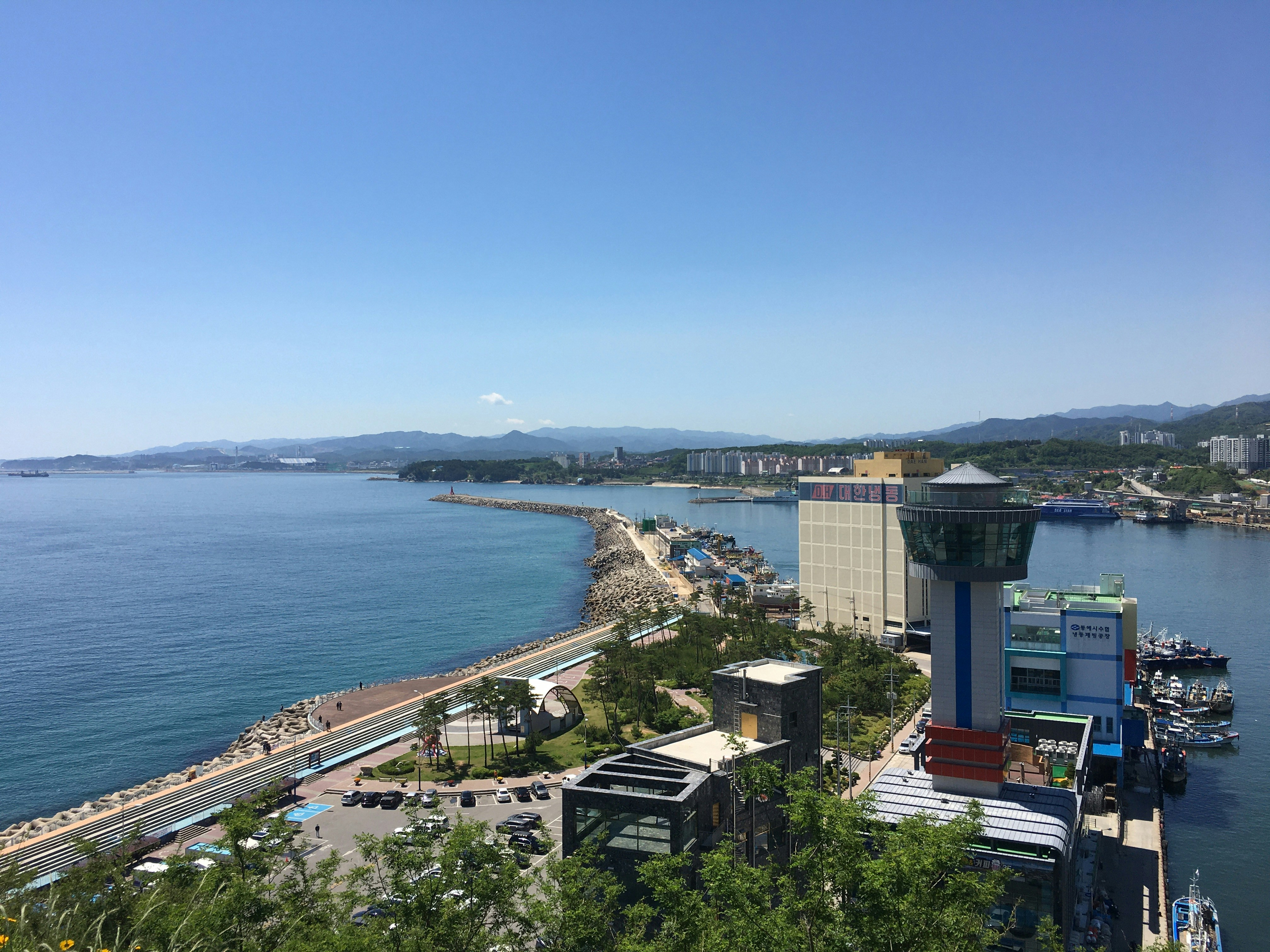 Expansive view of a coastal harbor with a mix of rocky shorelines and urban structures under a clear blue sky.