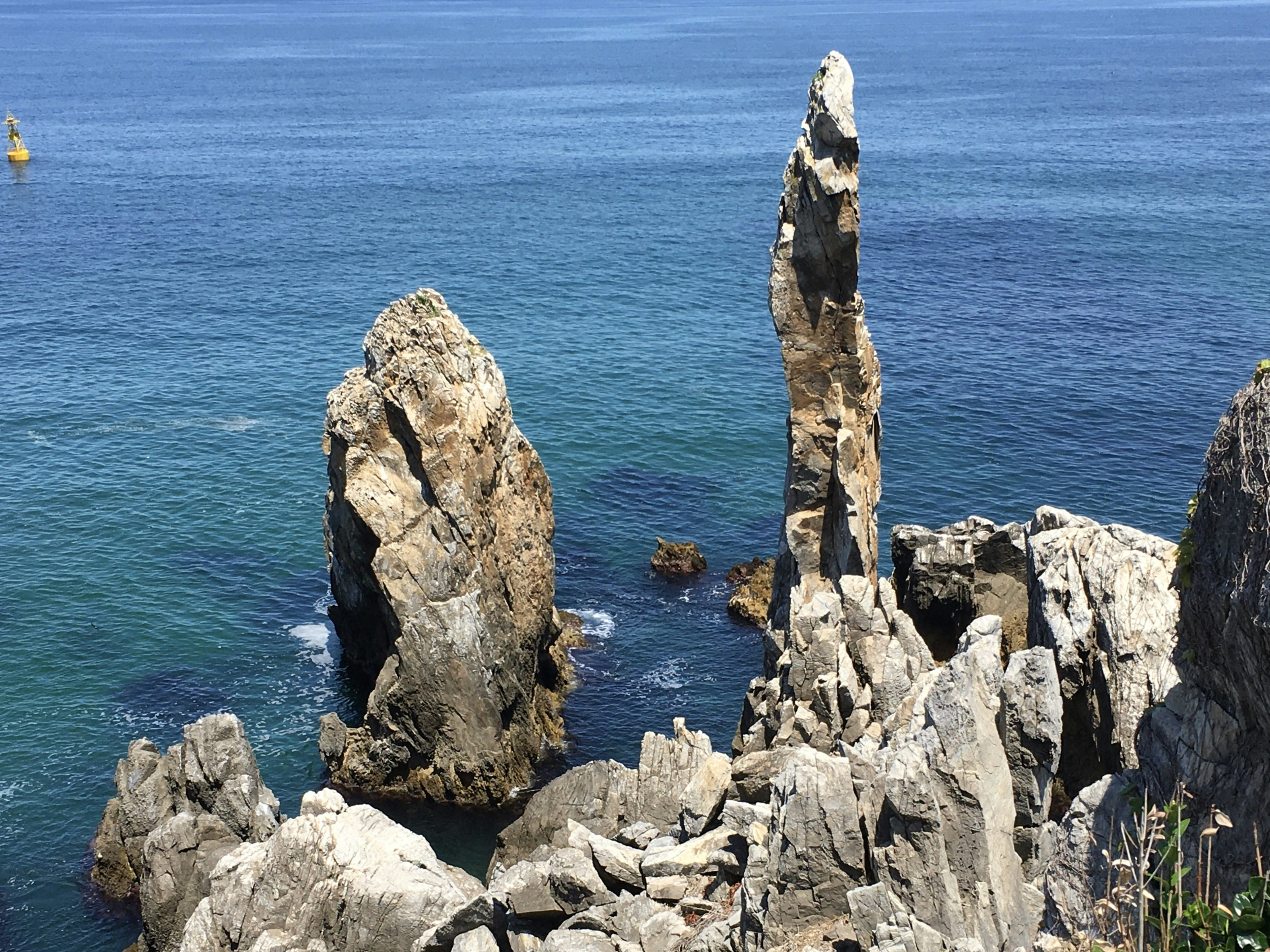 Two towering rock formations rise from the turquoise sea, showcasing the intricate patterns of erosion along the rugged coastline.