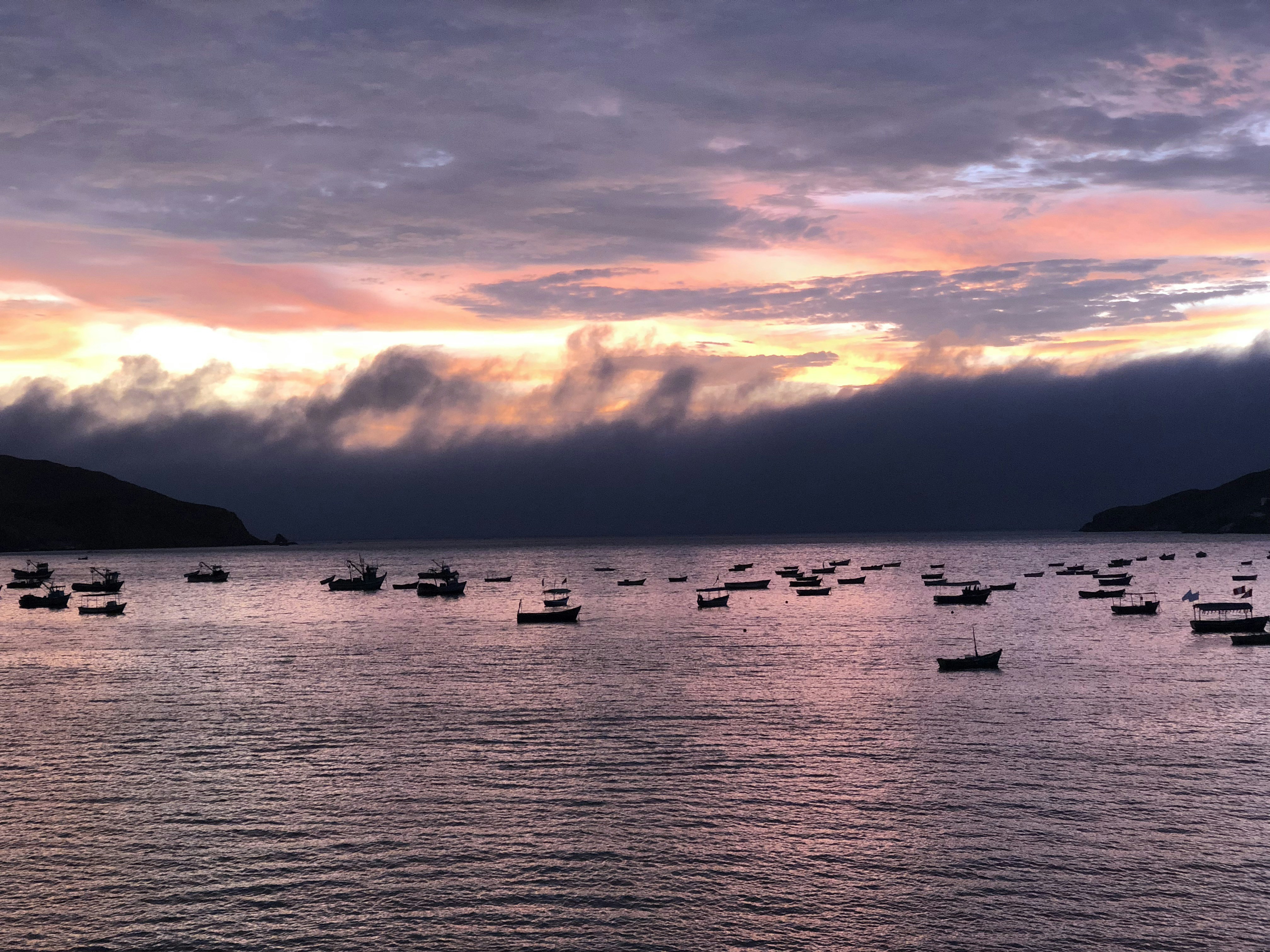 Boats rest on tranquil waters under a vibrant sunset sky with hues of pink and purple.