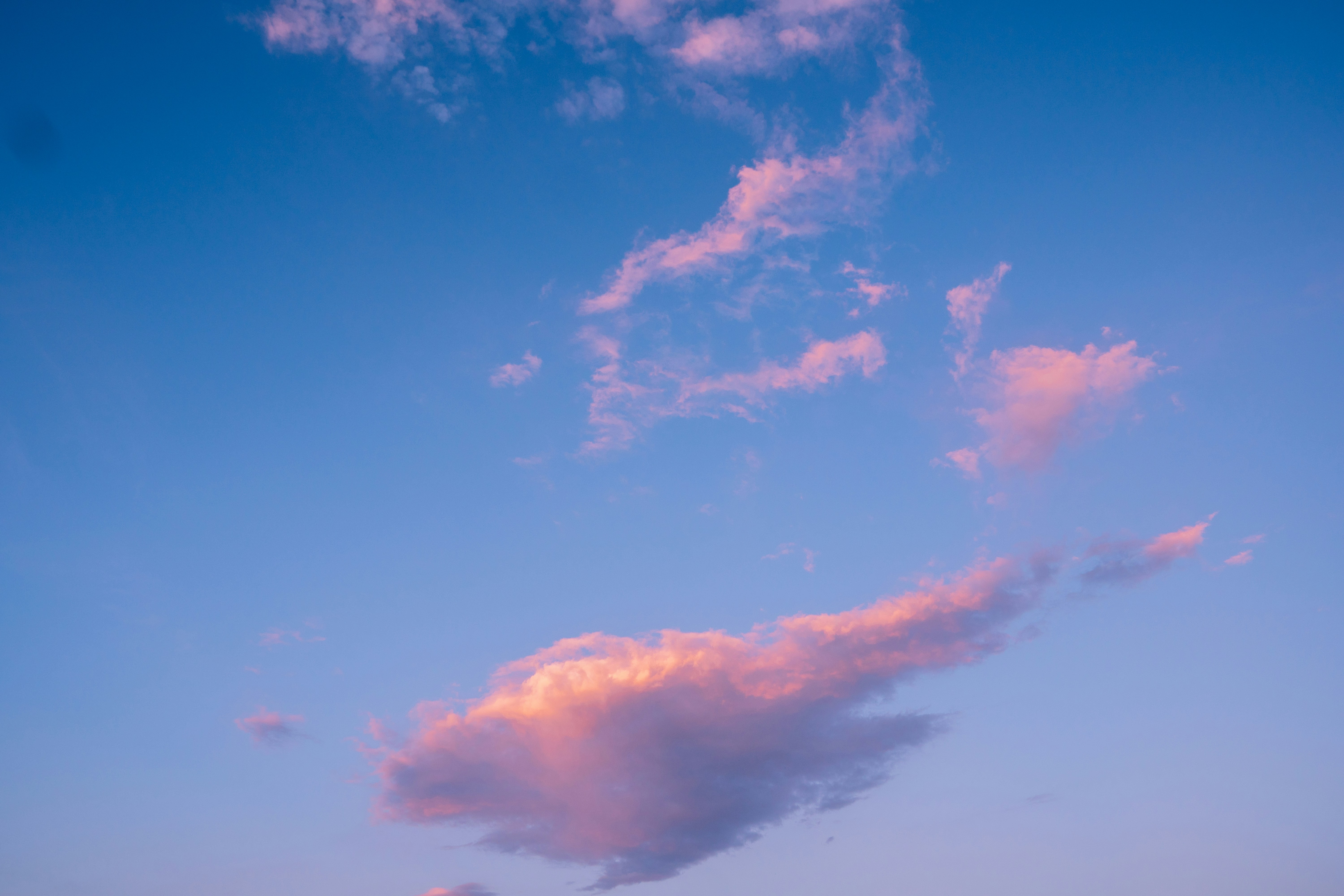 Soft pink clouds drift across a serene blue sky at dusk.