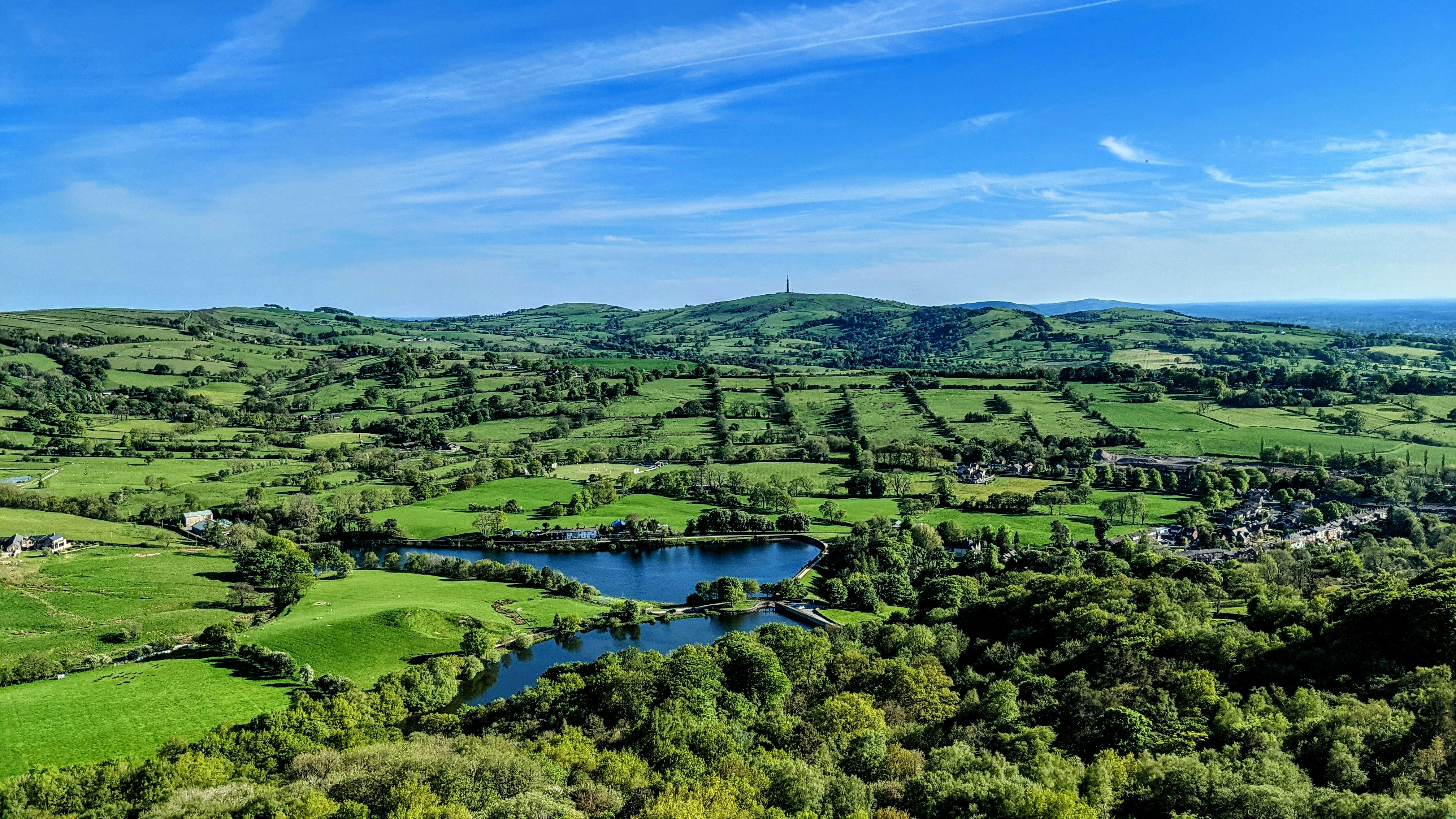 Rolling green hills and a shimmering lake under a clear blue sky in Cheshire.