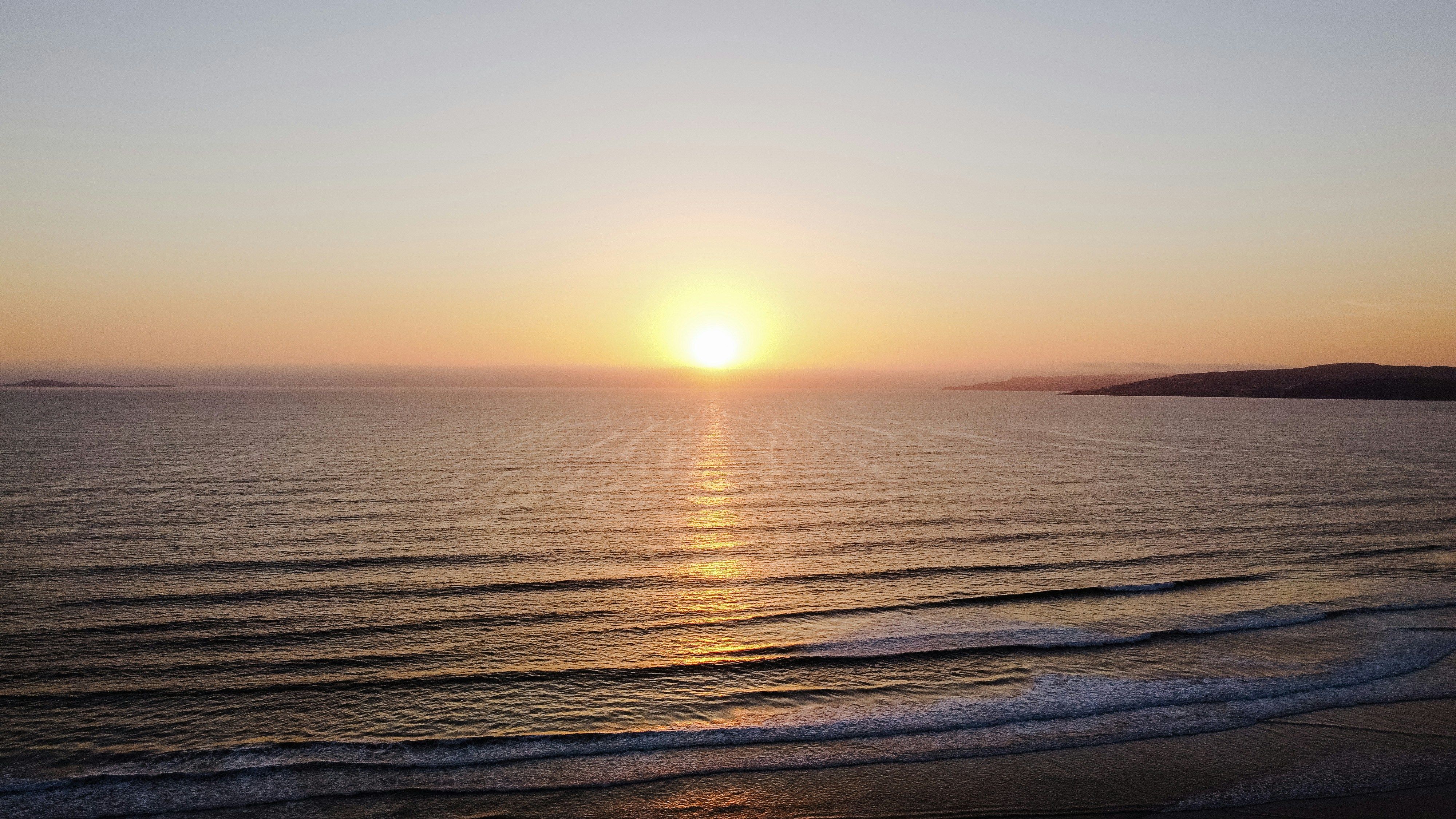 Golden sun setting over calm ocean waves, creating a serene atmosphere with soft reflections. 