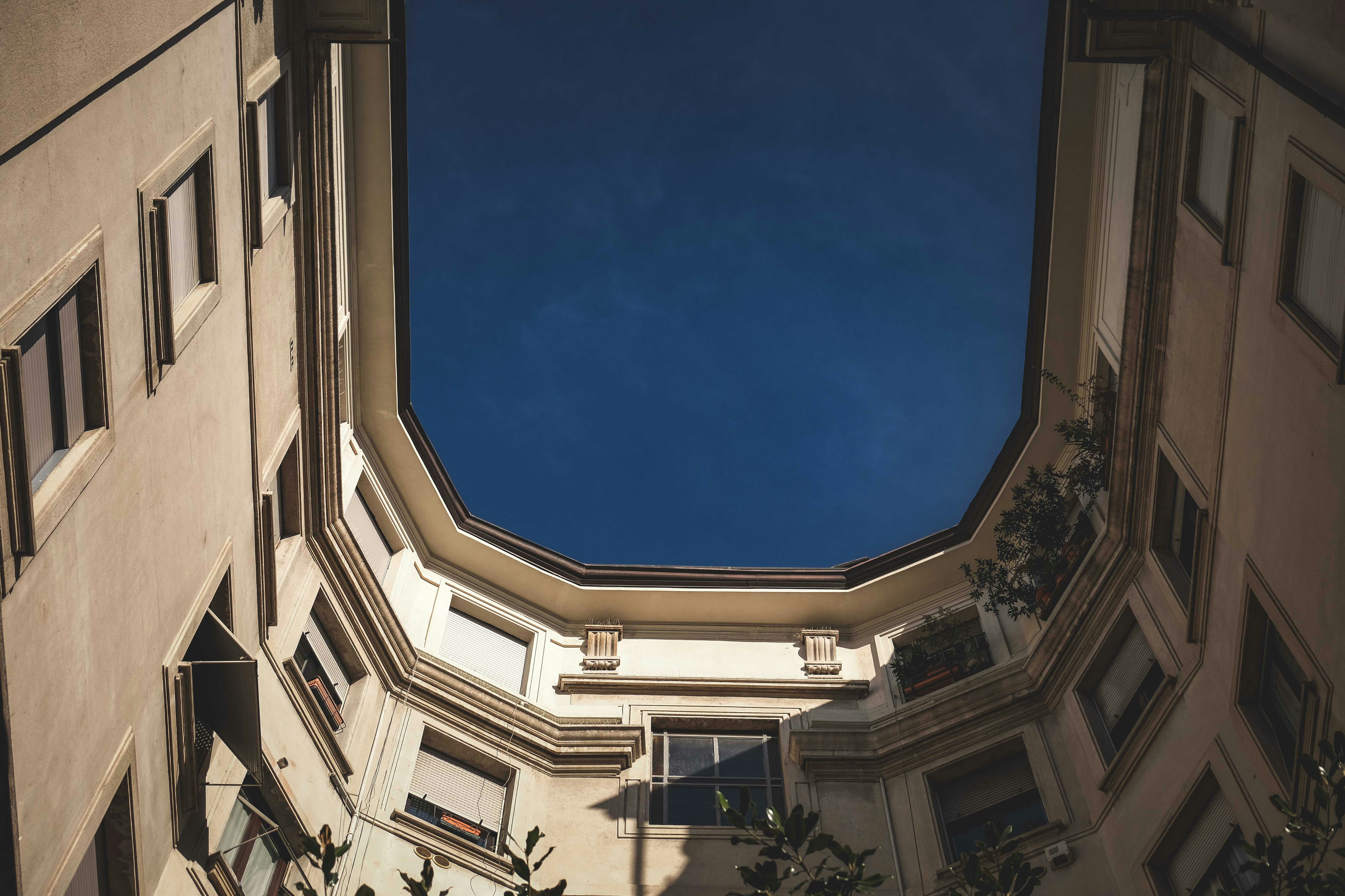 Looking up at the open sky framed by a circular courtyard of elegant architecture. The contrast between the building's structure and the blue sky creates a striking visual.