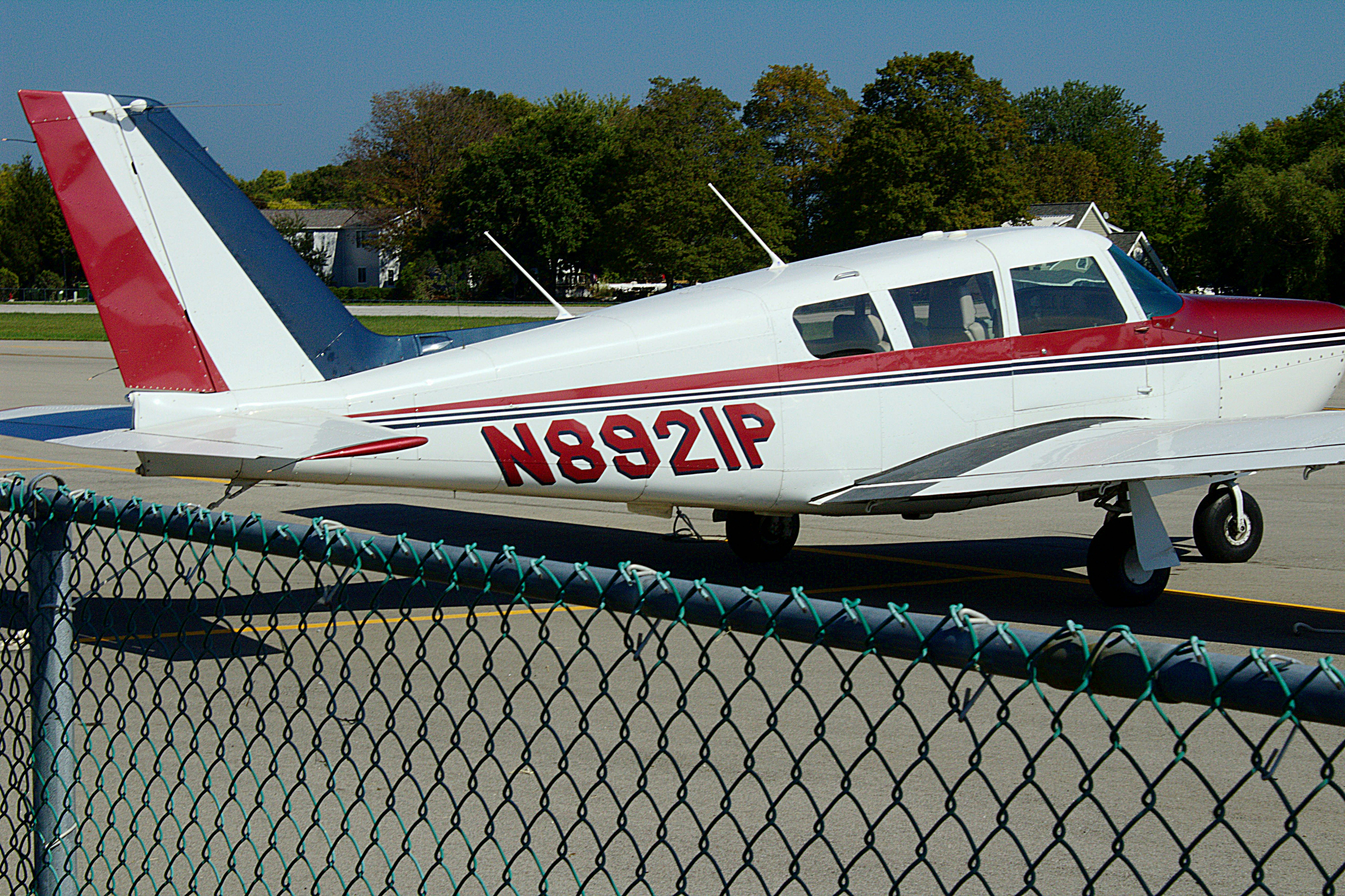 Single-engine aircraft N892IP parked on the tarmac, showcasing its sleek design and vibrant color scheme against a backdrop of trees.