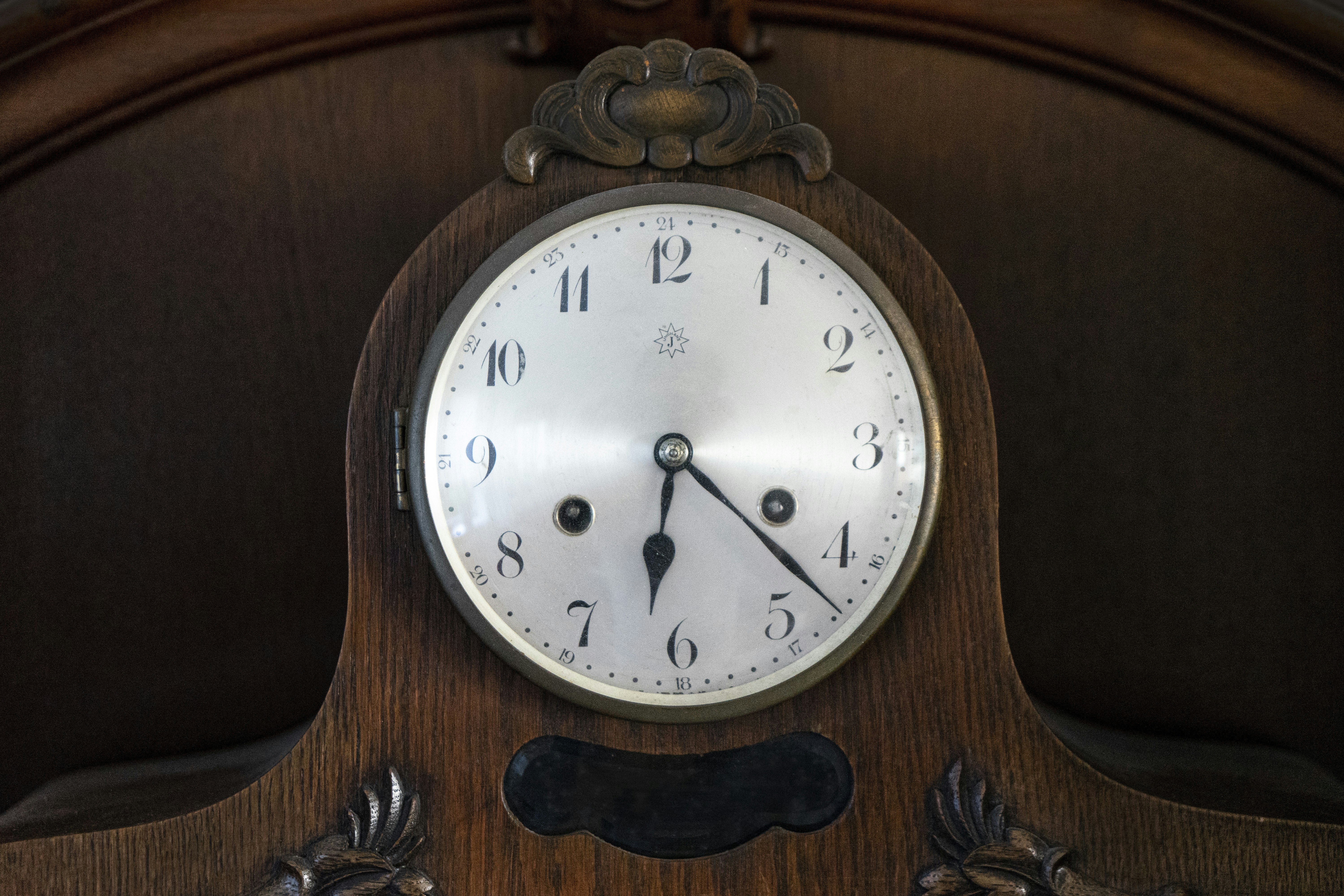 Antique wooden wall clock with ornate carvings and Roman numerals.