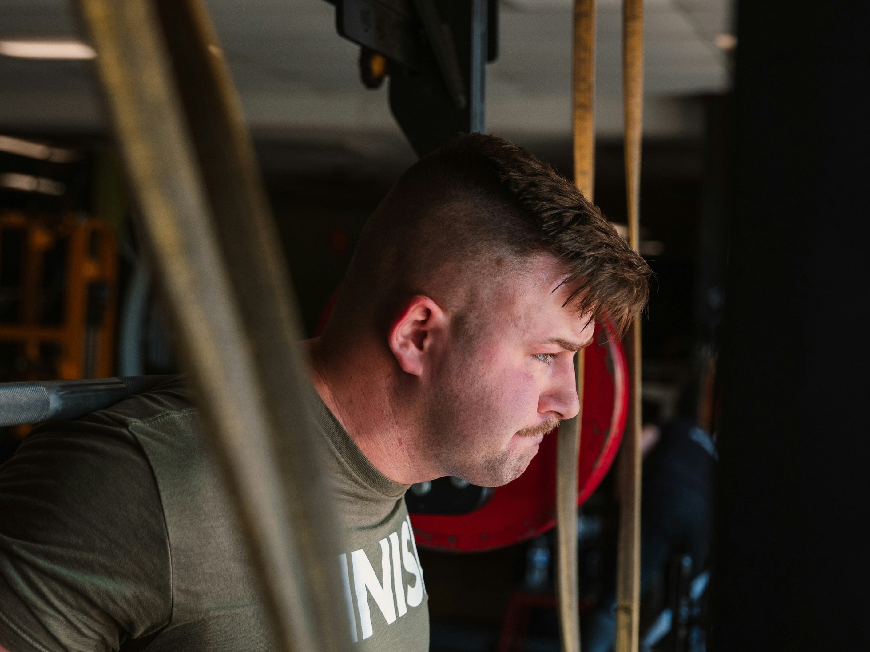 Man in a gray shirt concentrating during a workout in a gym setting.